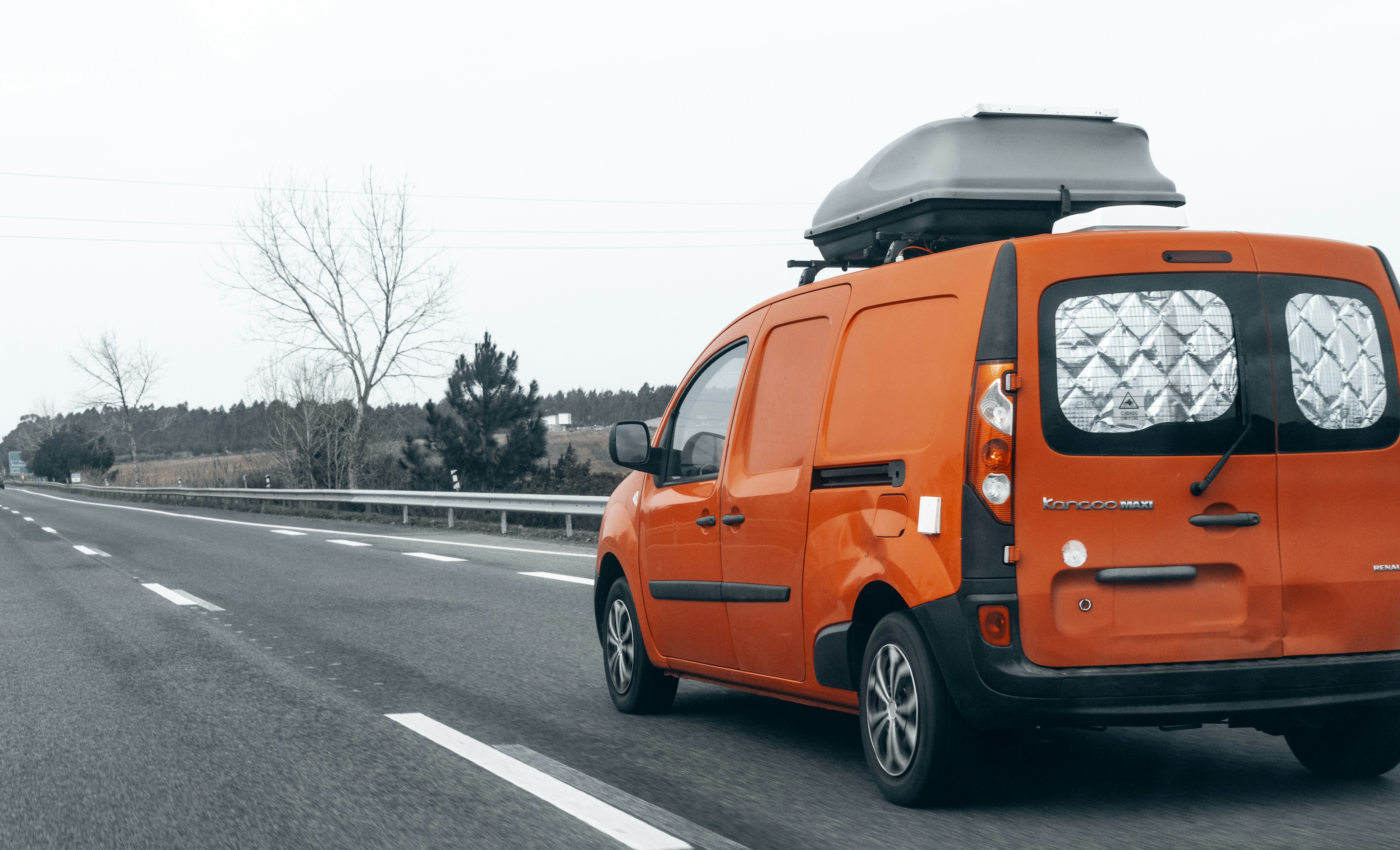 Orange utility van on a quiet highway with a roof cargo box