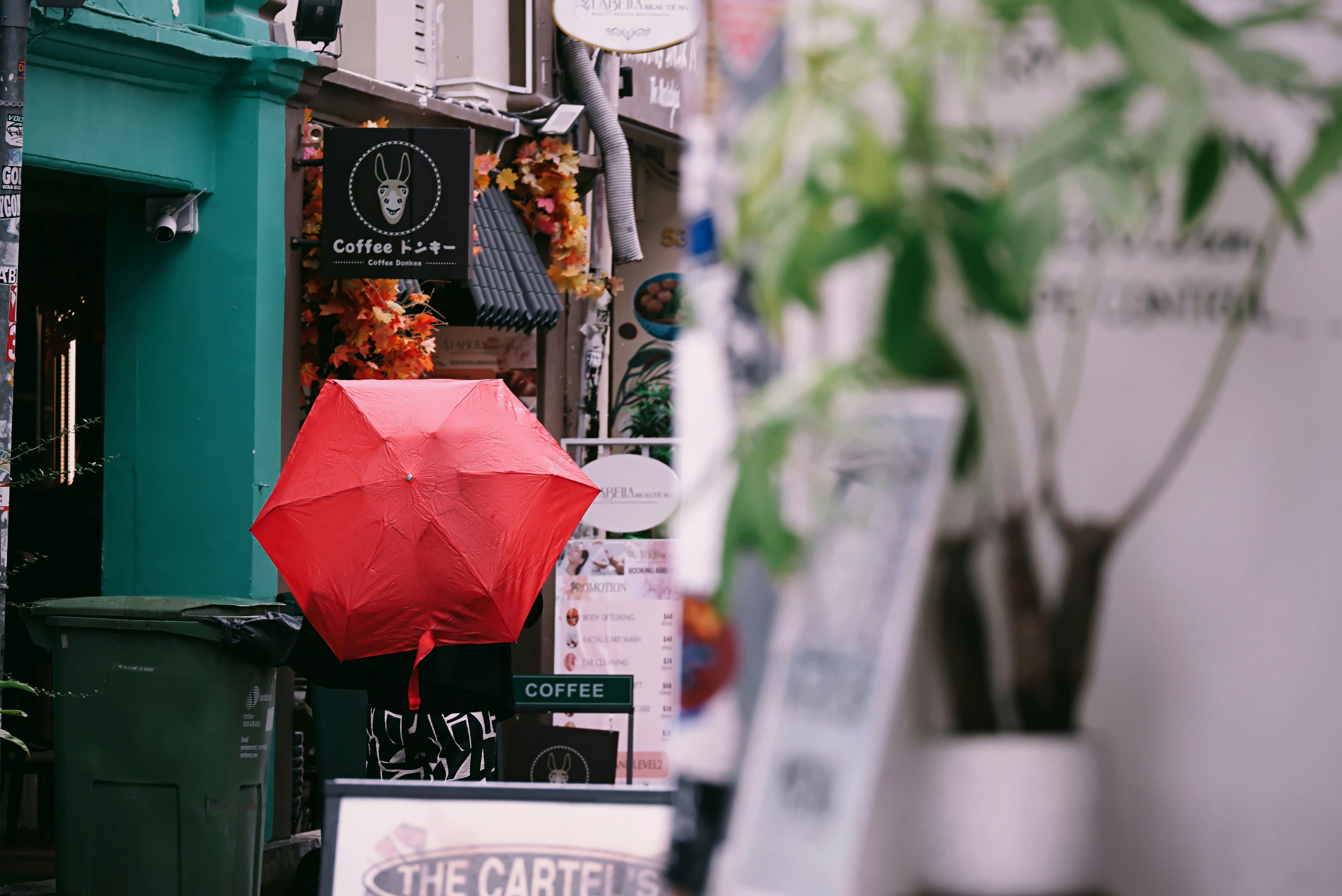 Red umbrella over a cozy café doorway on a rainy city street