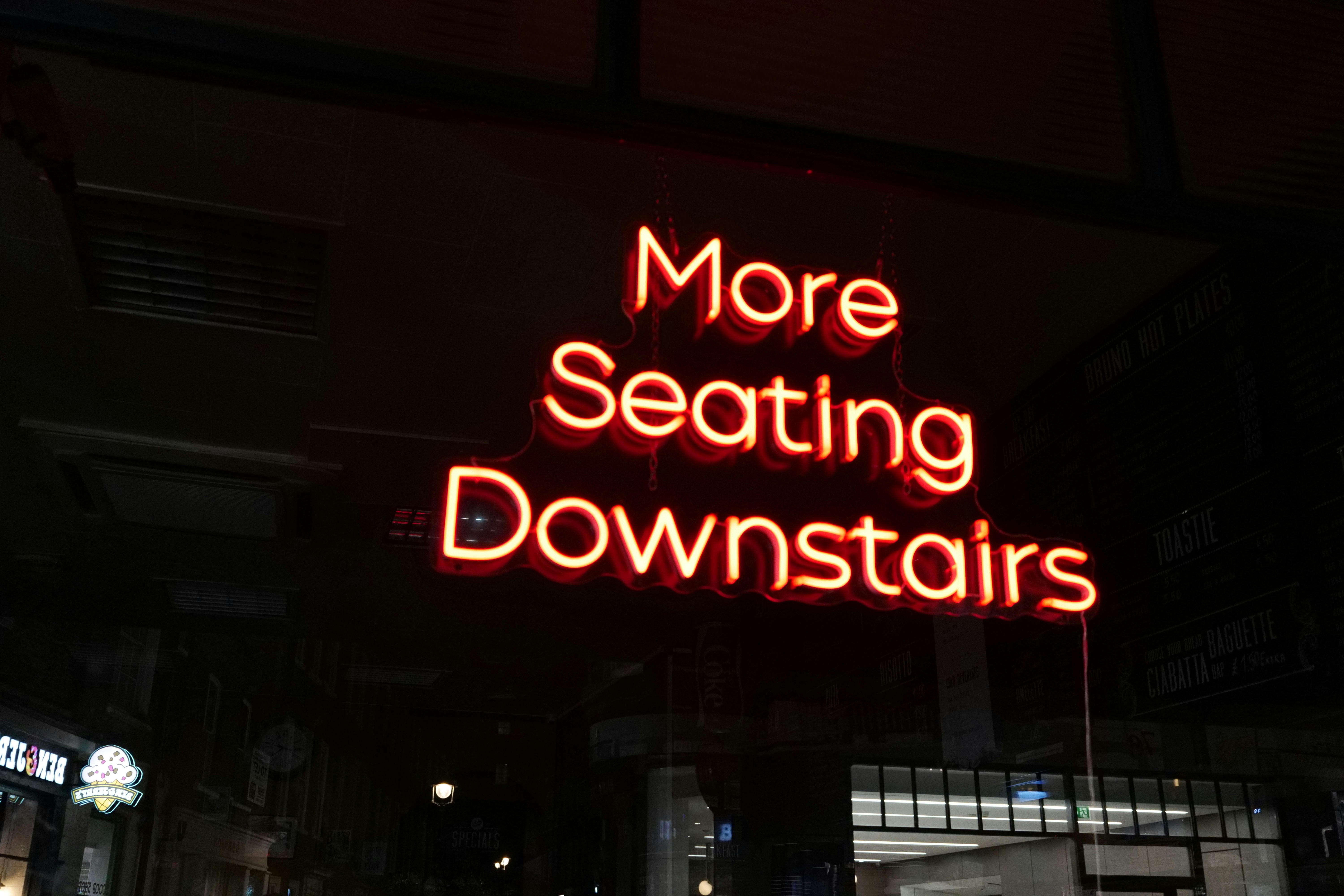 Neon Sign Over Dark Venue: More Seating Upstairs
