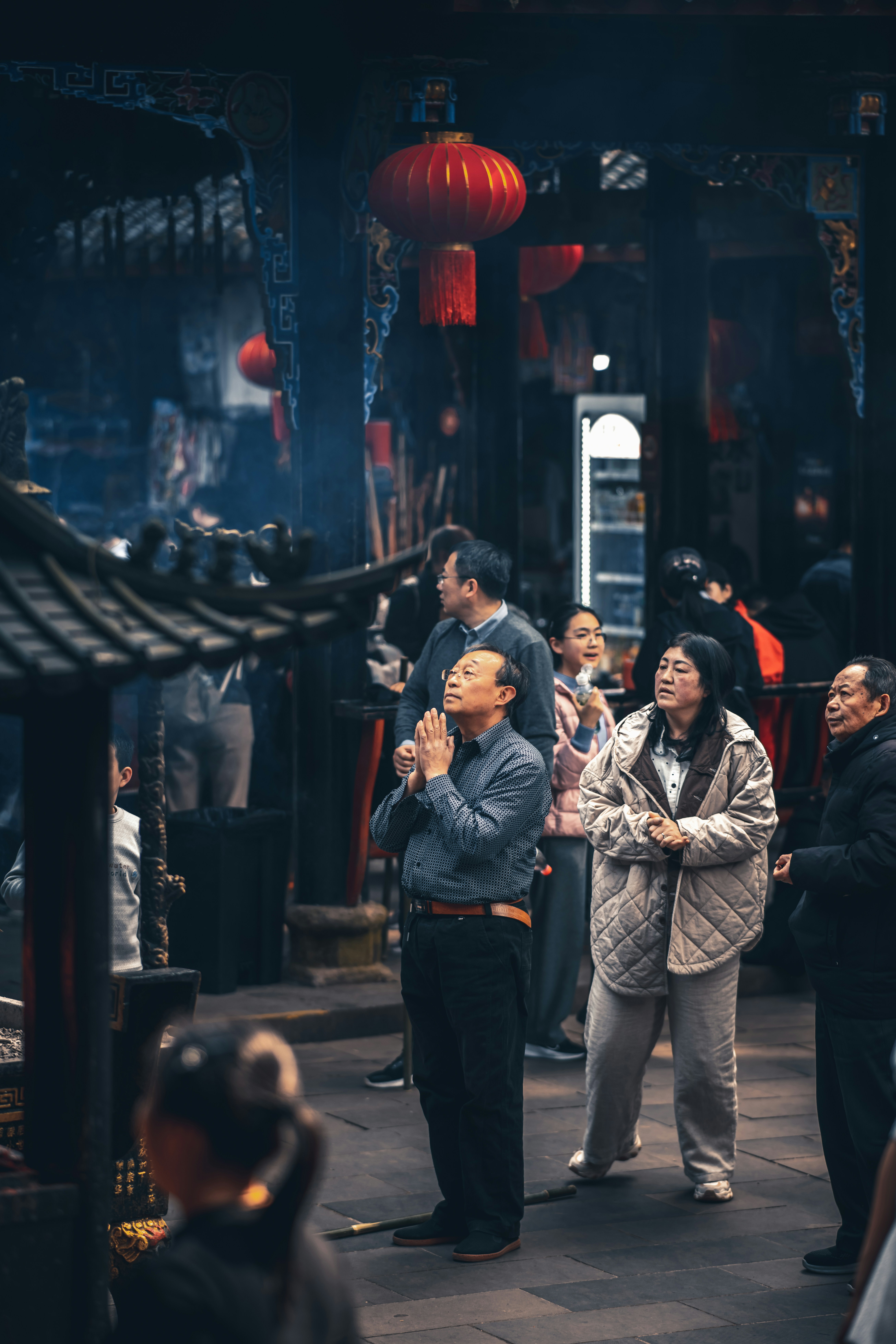 Prayerful Pause Beneath Red Lanterns in a Quiet Corridor