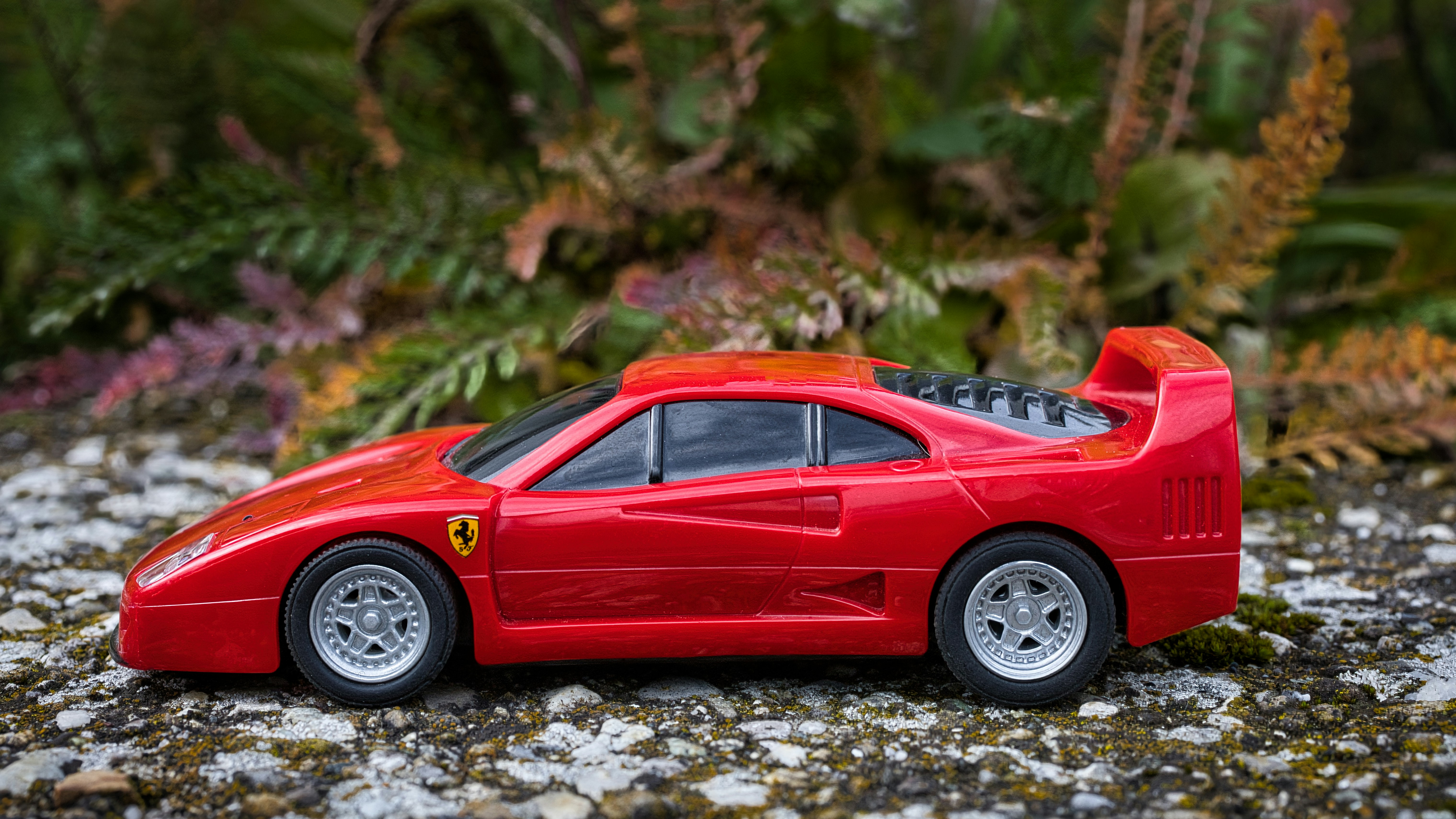 Red Icon on Rough Ground: A Scale Model Ferrari Resting on Mossy Gravel