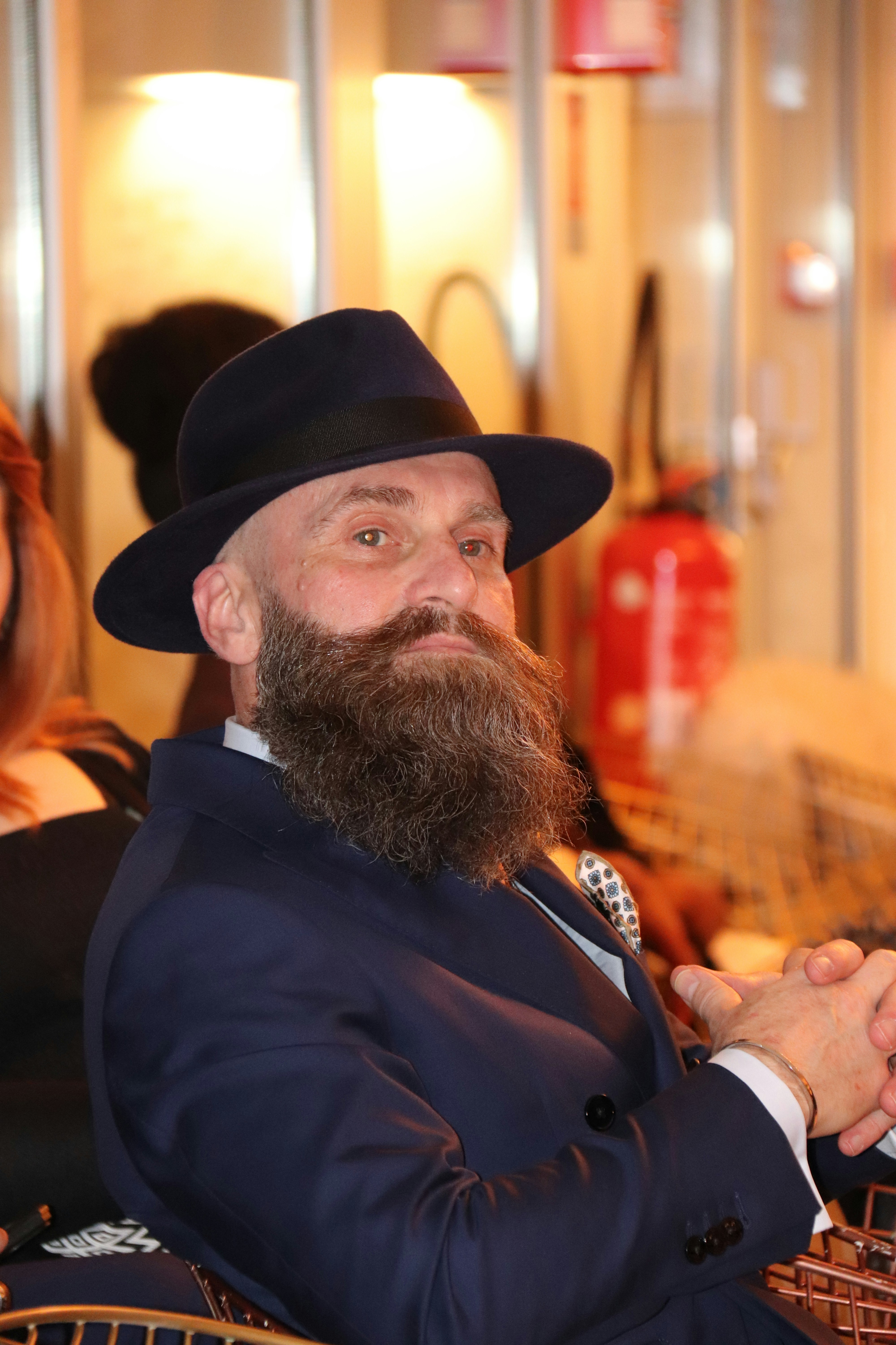 Gentleman in a navy suit with a full beard at a dim, indoor gathering