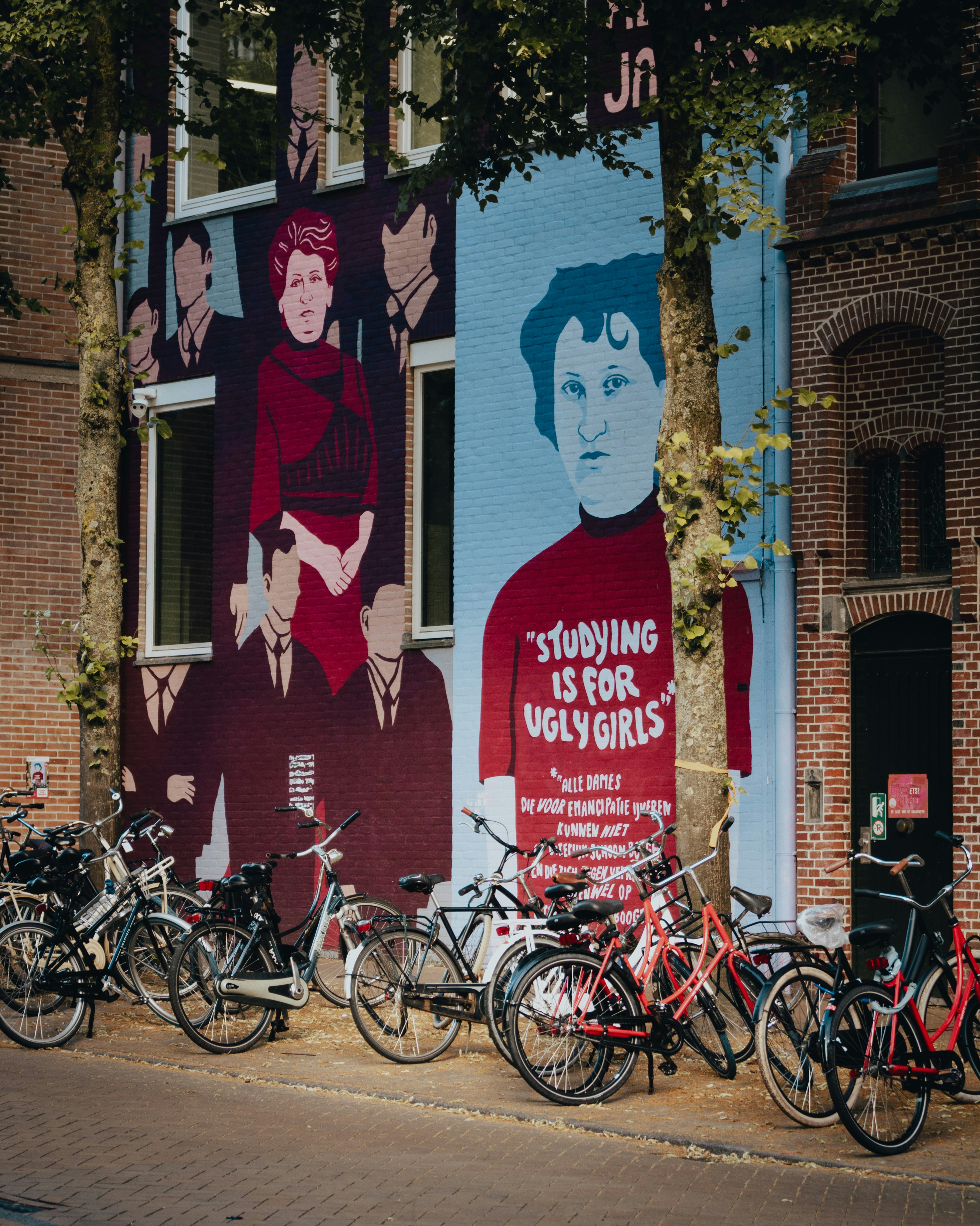 Portraits on brick: mural with bold red and blue figures under urban trees
