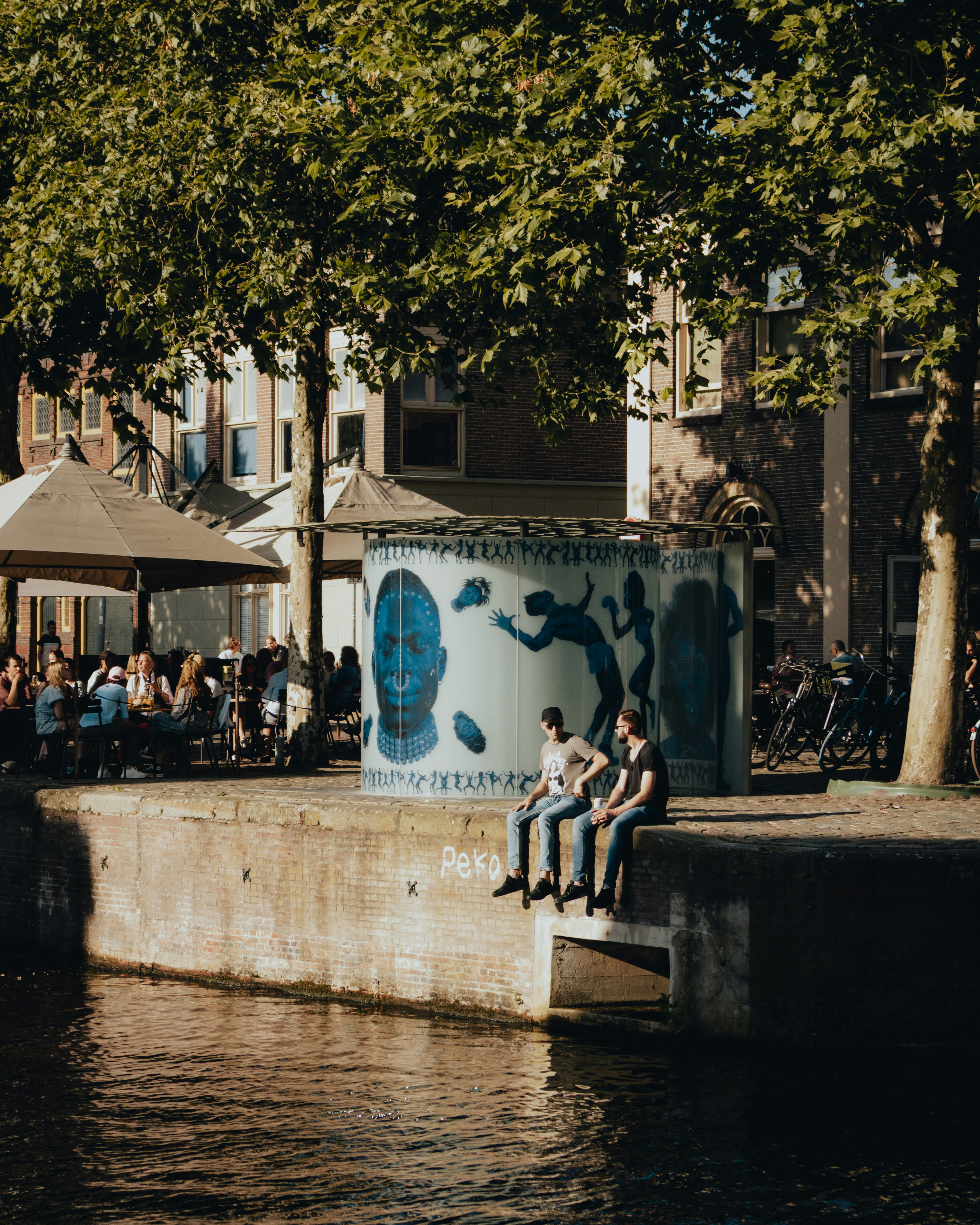 People by the canal: afternoon buzz near a mural and cafe