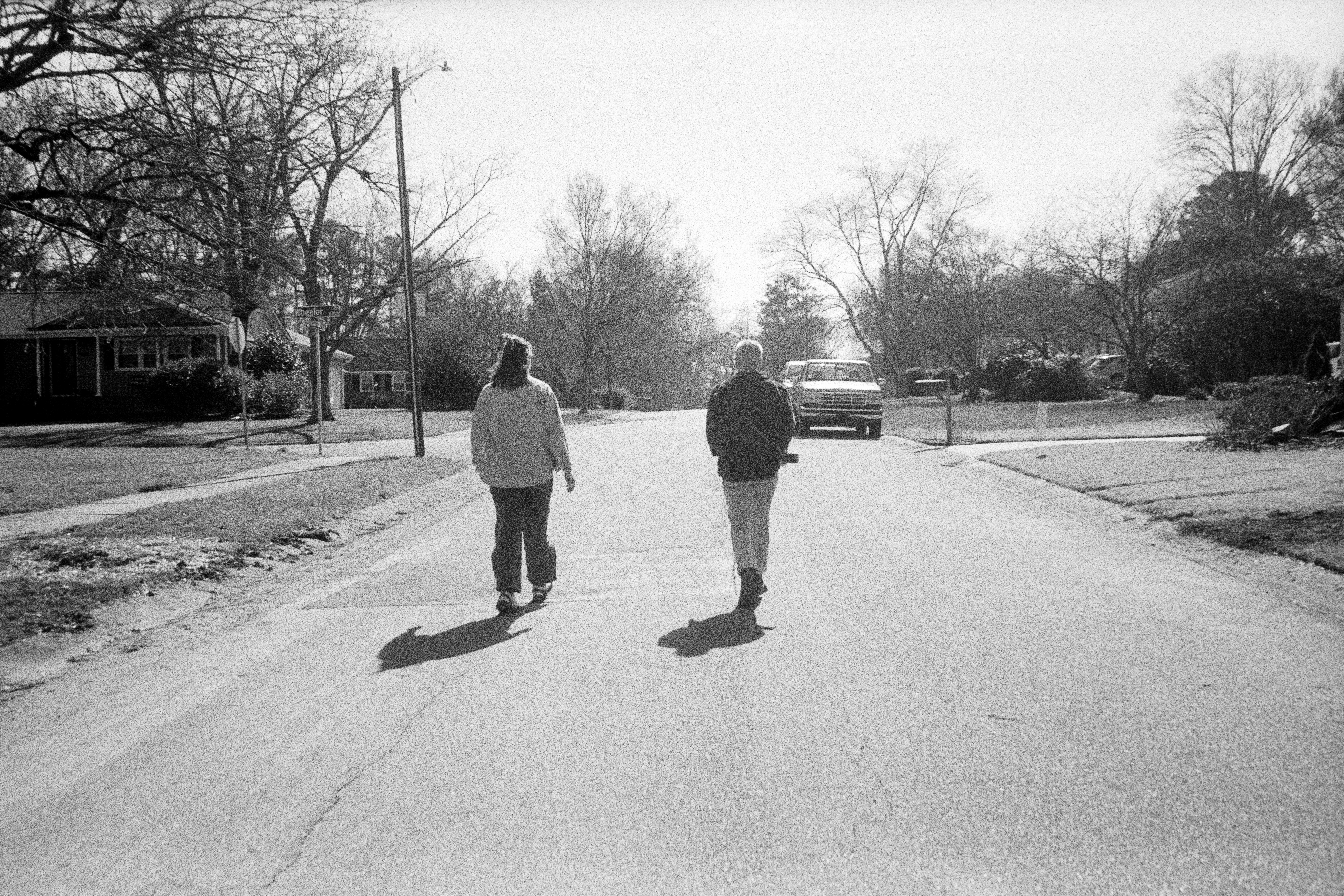 Two pedestrians stride toward a sunlit suburban horizon