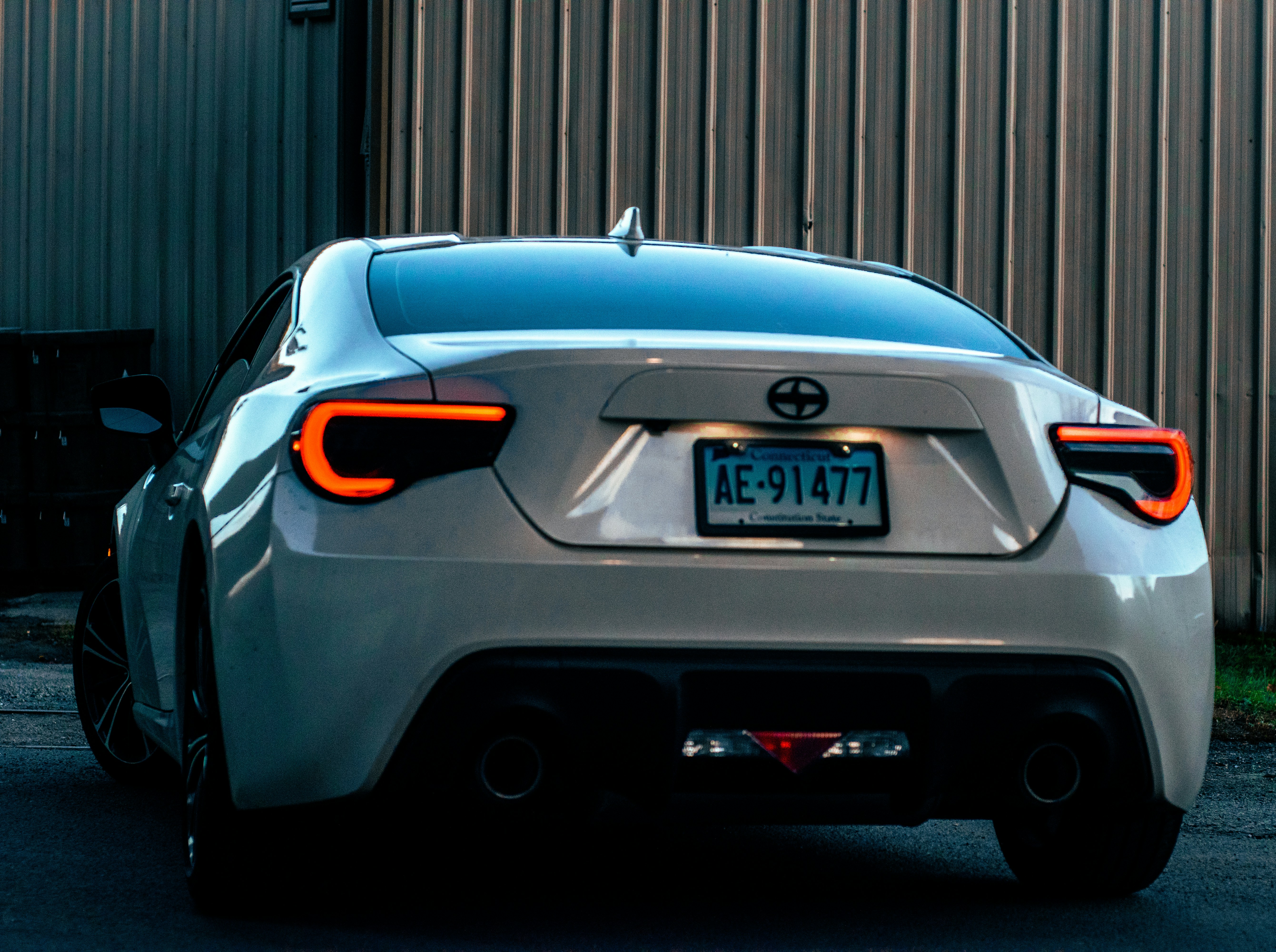 Rear View of a White Sports Coupe with Dual Exhausts in an Industrial Lot