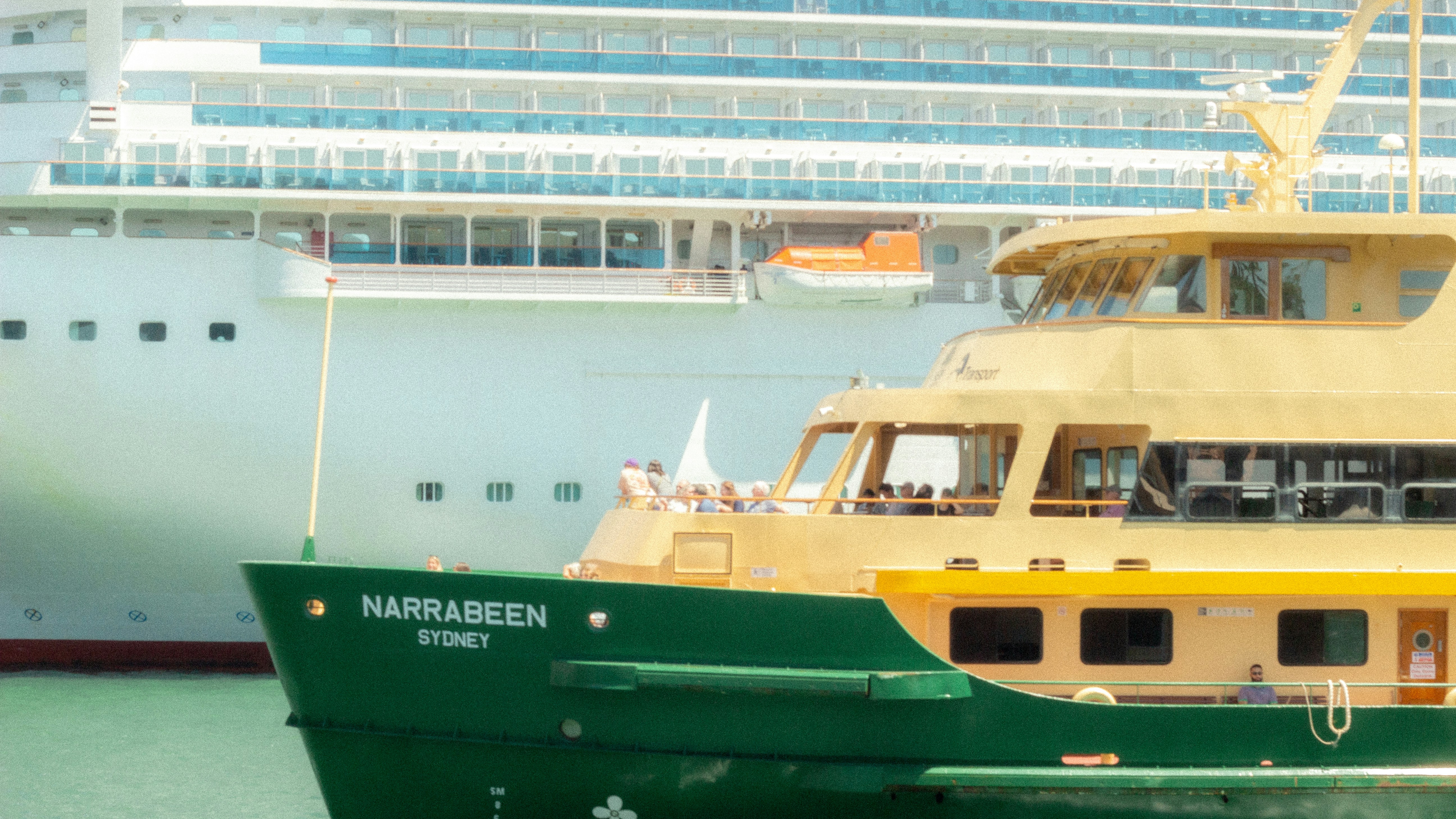 Green and Yellow Ferry Docked Against a Grandeur Cruise Ship
