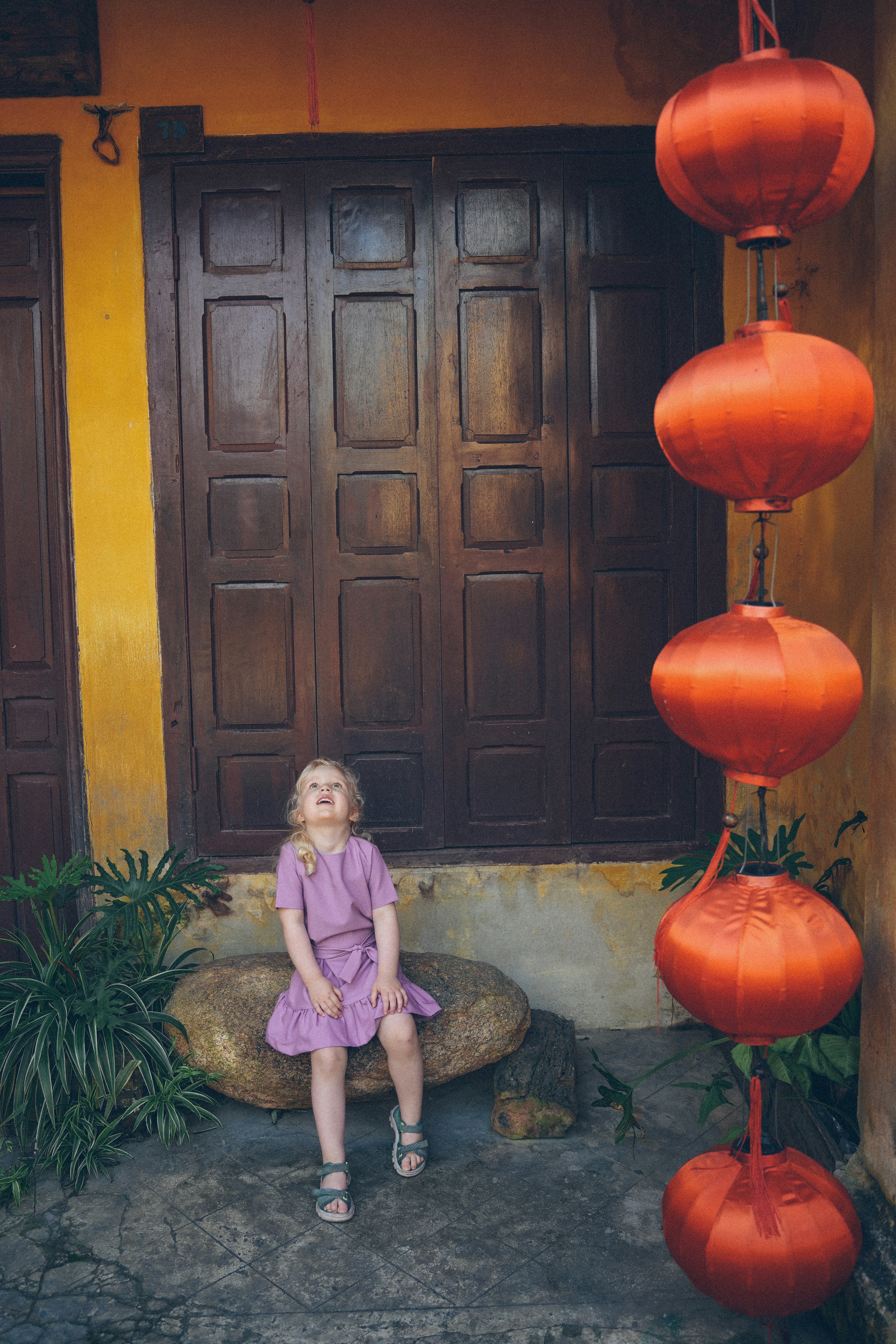 Lilac Dress, Red Lanterns: A Child’s Quiet Moment by the Door