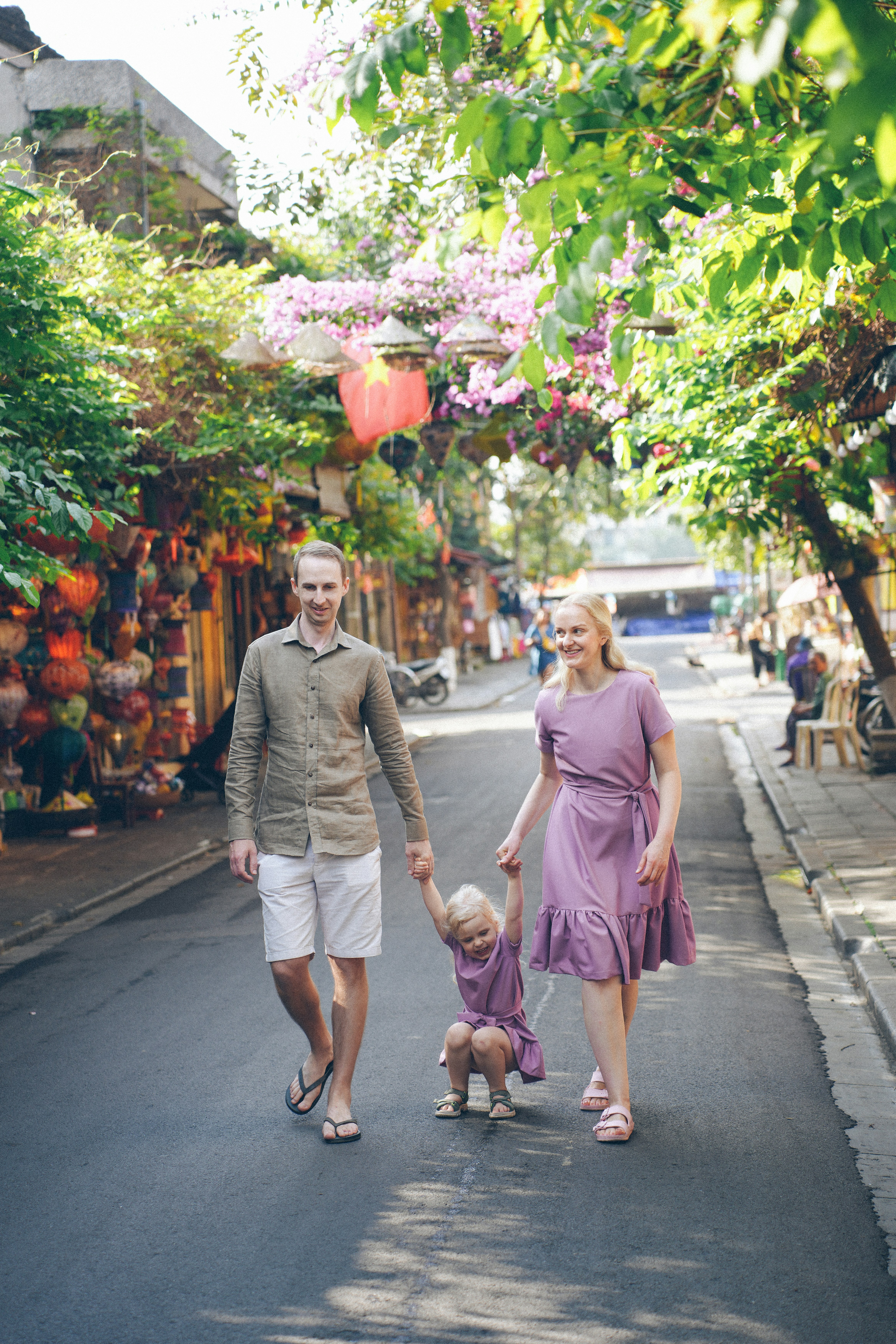 Sunlit Street Portrait: A Young Family Stroll Under Flowering Canopy