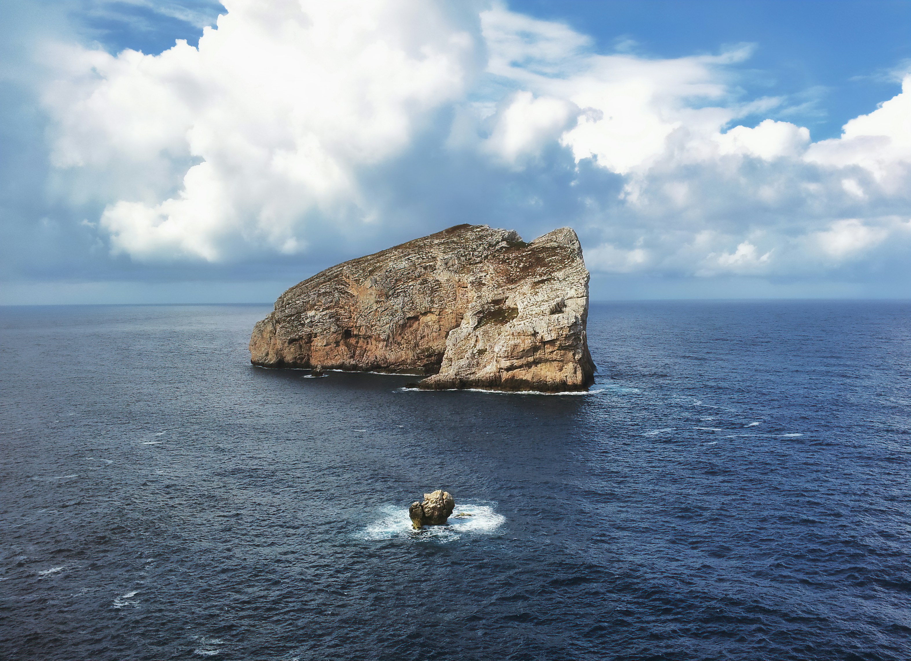 Large rock island in the blue ocean under clouds
