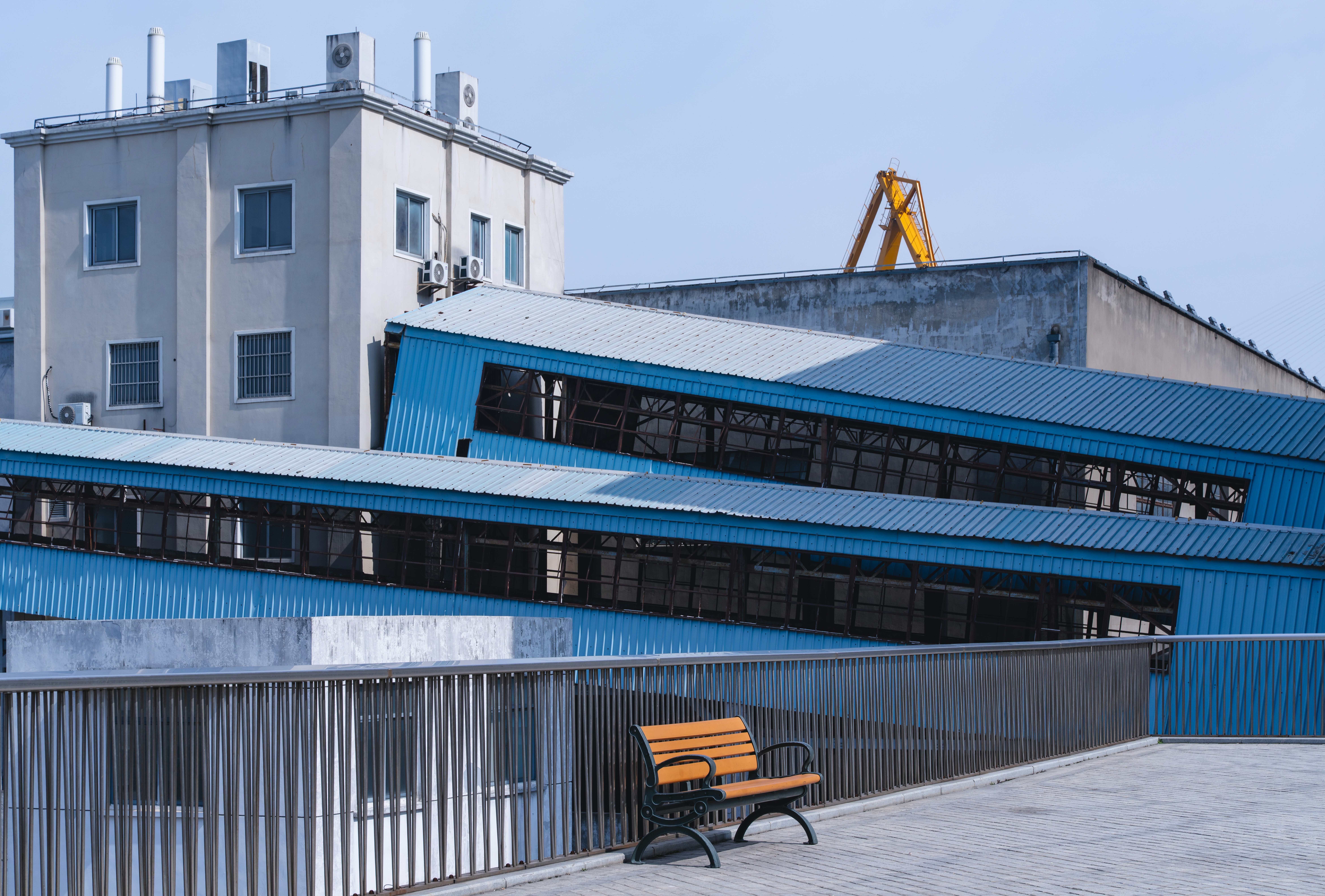 Blue Roofs, Concrete Lines: An Idle Bench Beneath an Industrial Sky