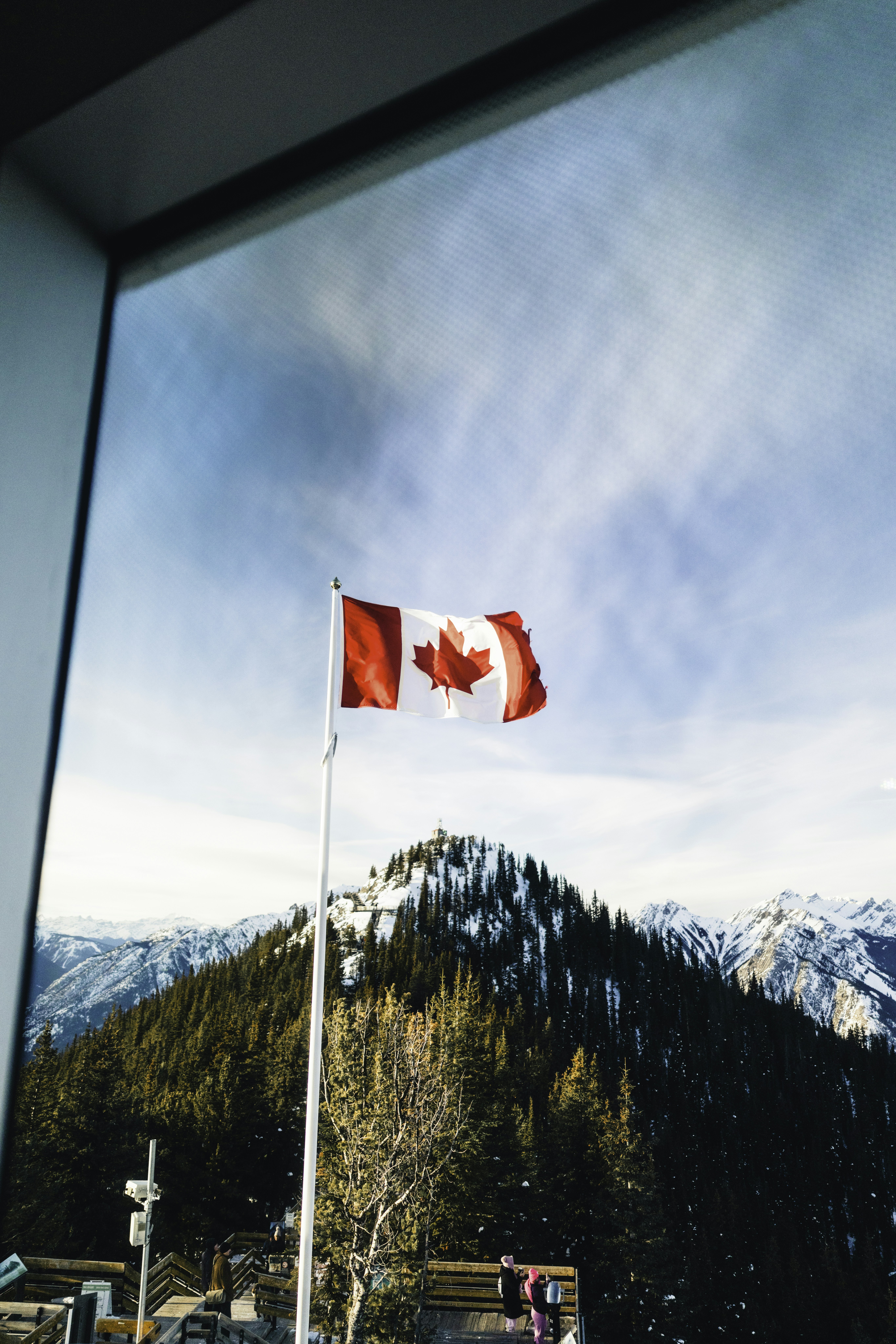 Flag Over Snowy Peaks: Canadian Pride Framed by Window Glass