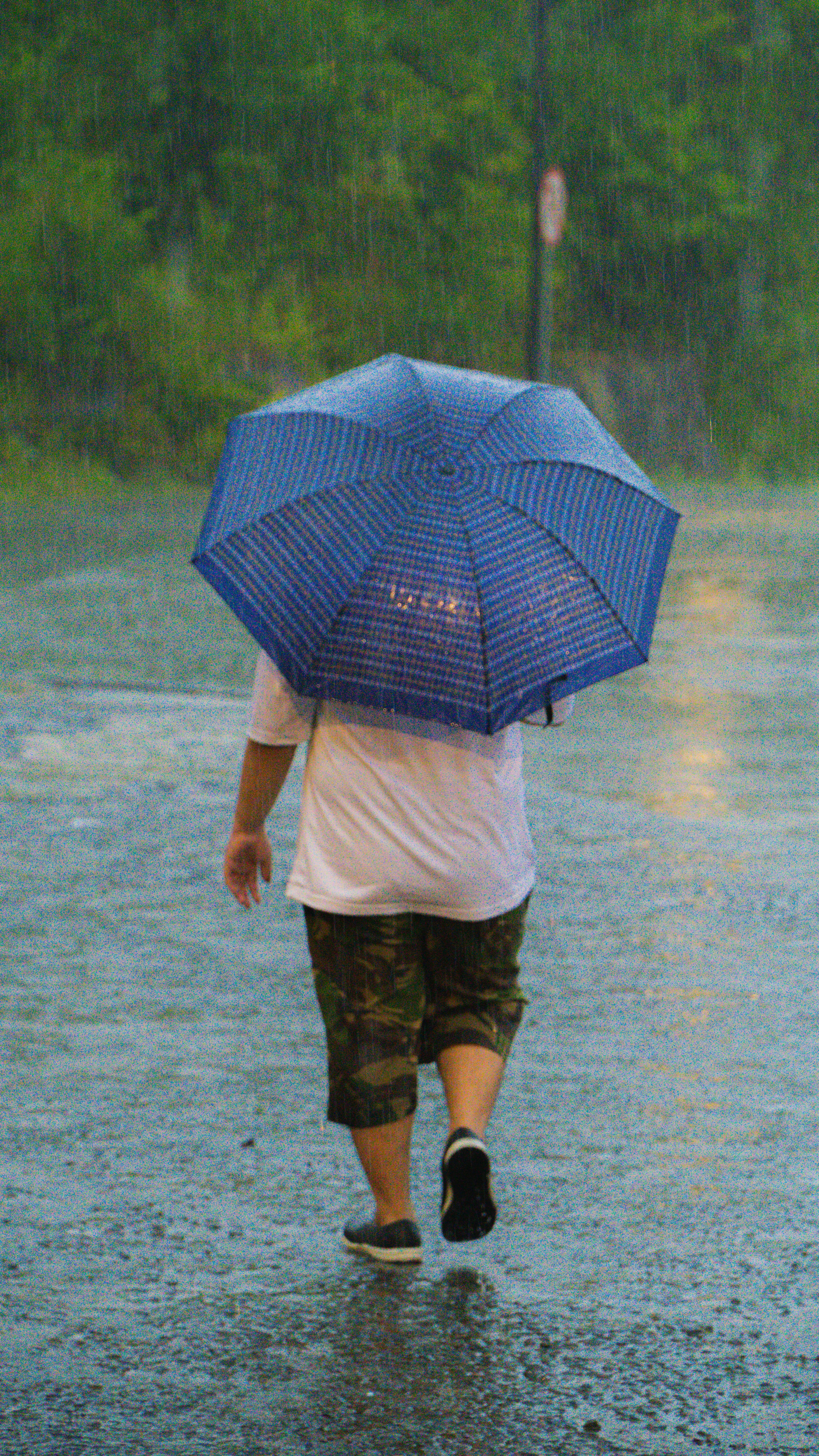 Blue Umbrella in the Rain: Lone Wanderer Across a Wet Parking Lot