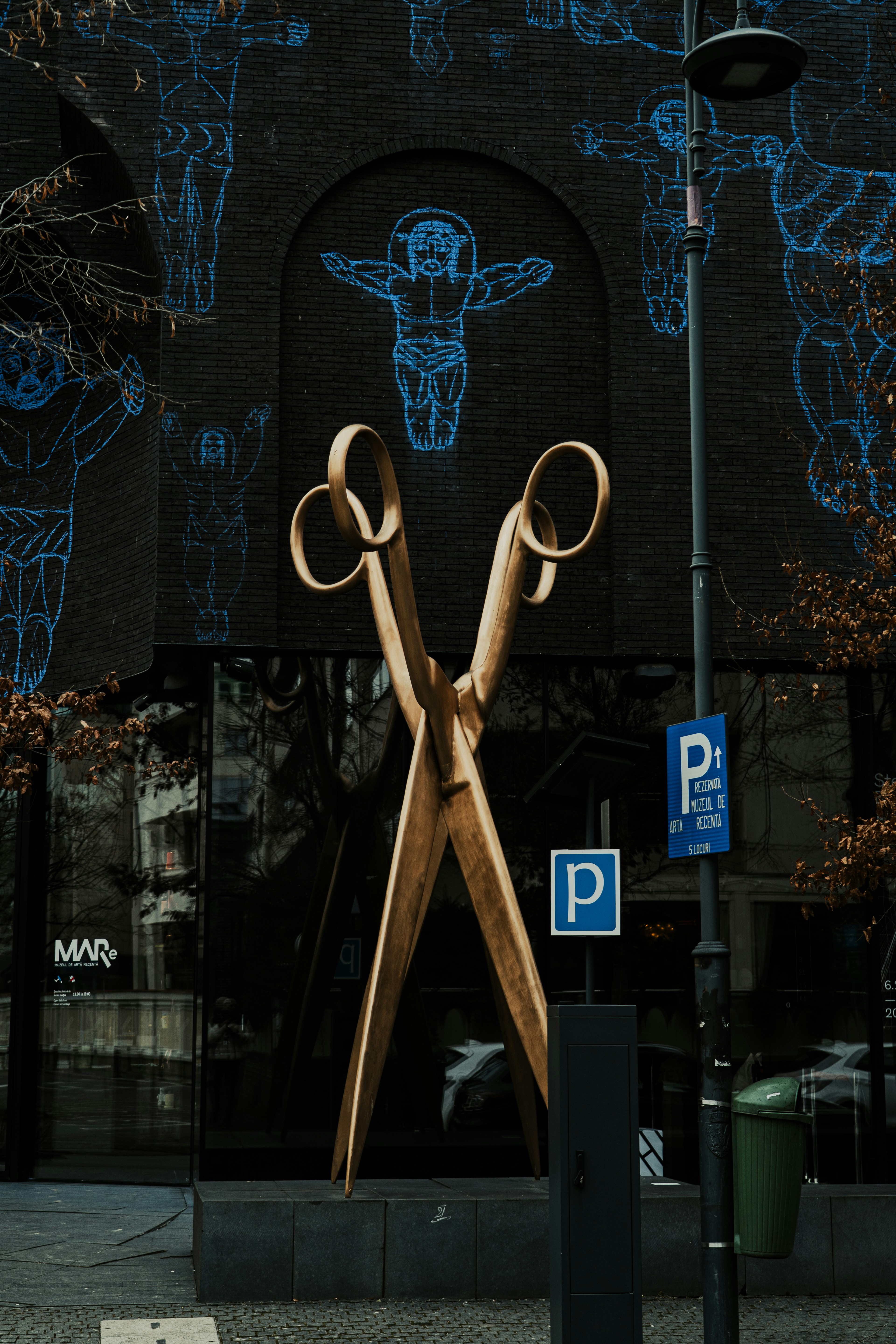 Gilded Scissors Tower: Urban Sculpture Framing the Neon-Blue Graffiti
