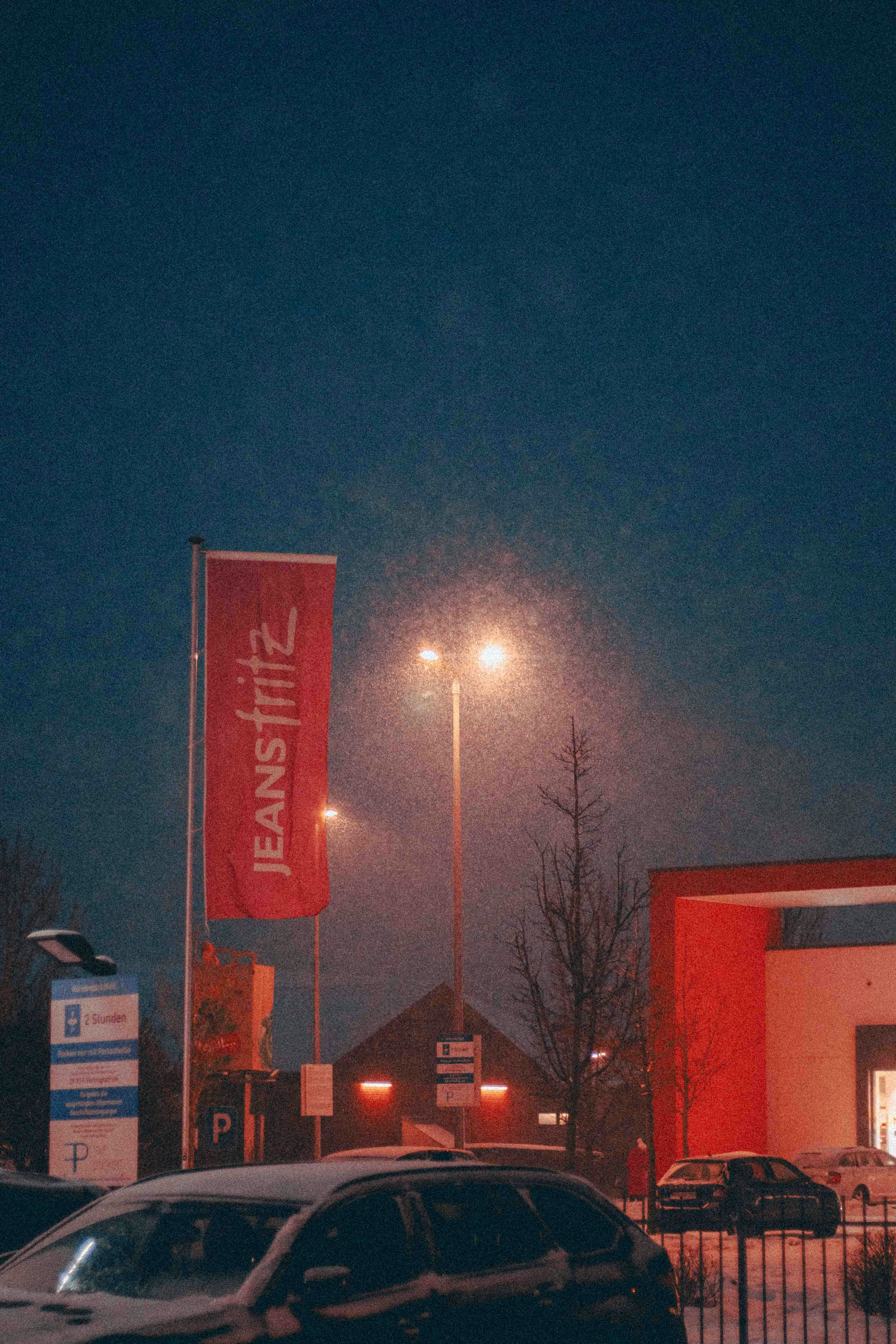 Neon-lit street at dusk with a red storefront flag and parked cars