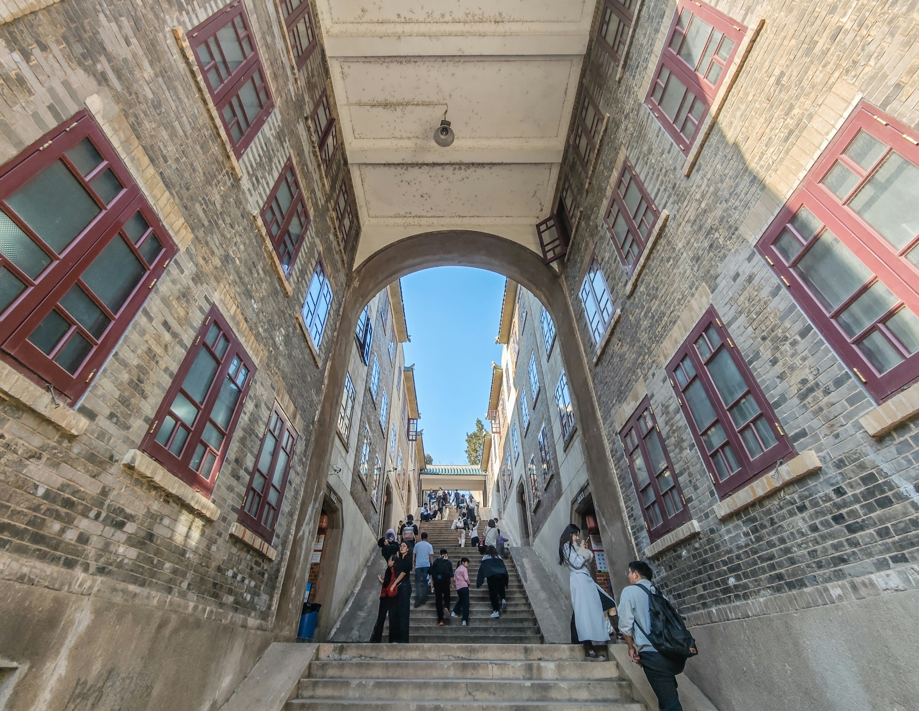 People ascend stairs under arched brick buildings