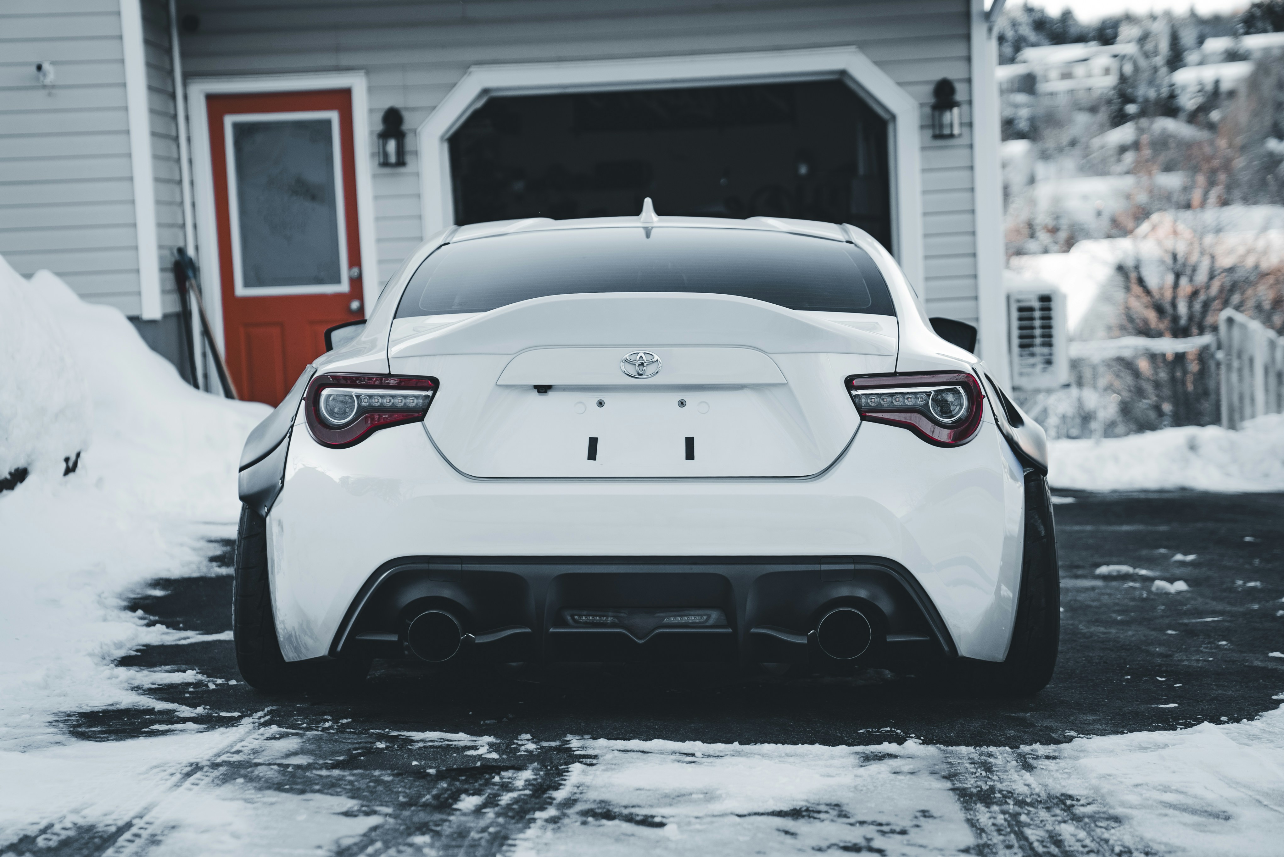 White sports coupe at winter driveway, rear view with snow banks