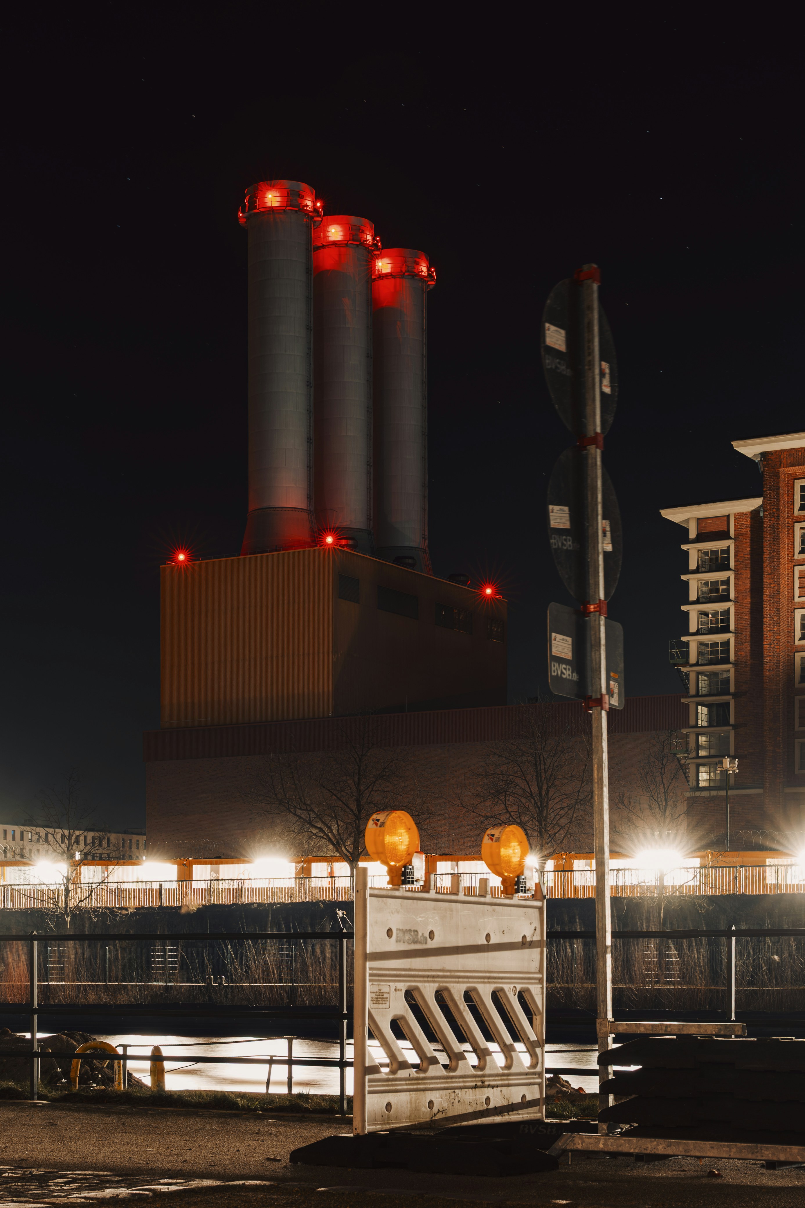Industrial nightscape: three red-lit chimneys looming over a dimly lit construction site