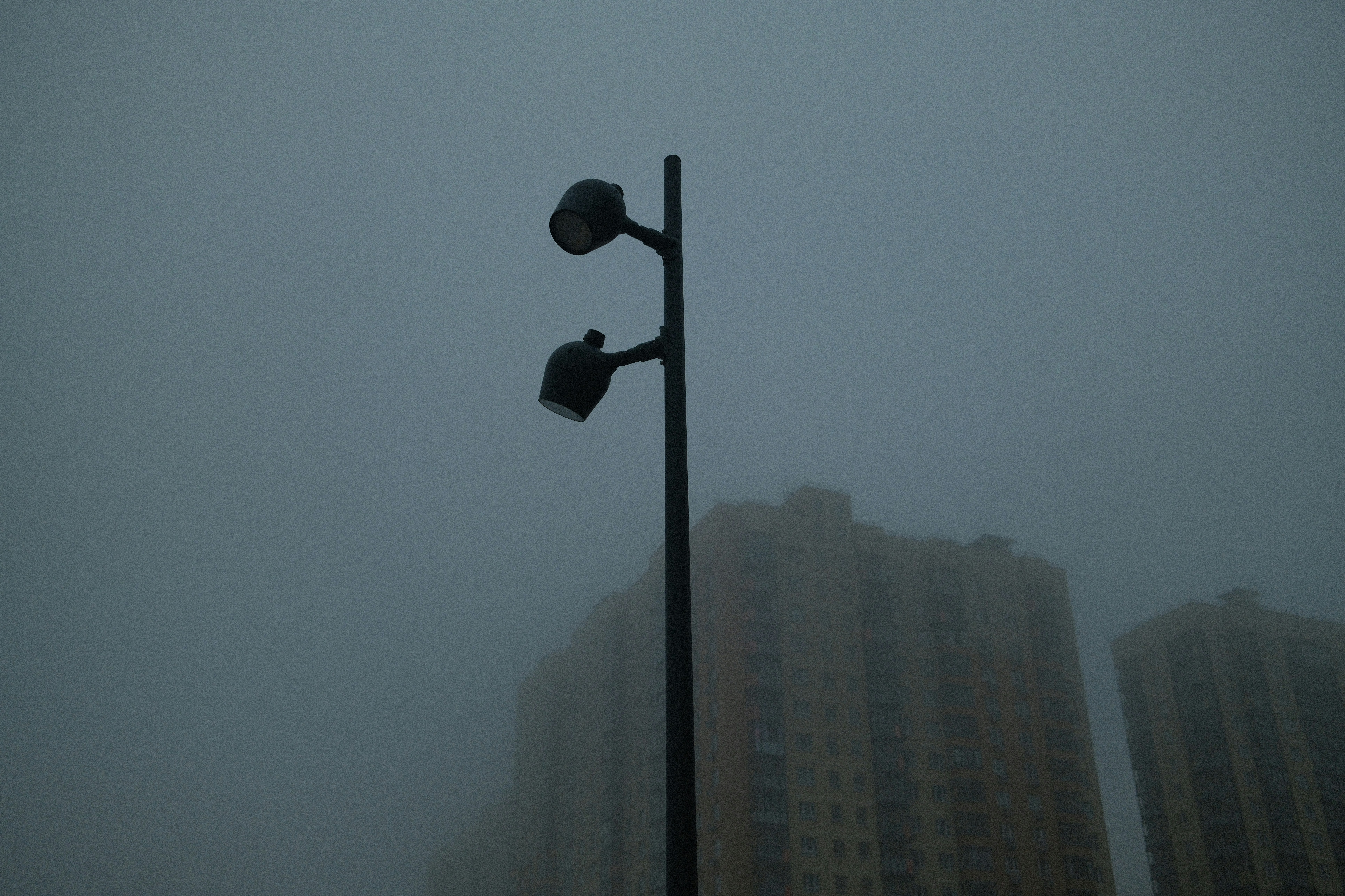 Fogbound Lantern: A Mono-Lit Streetlamp Against Distant Towers
