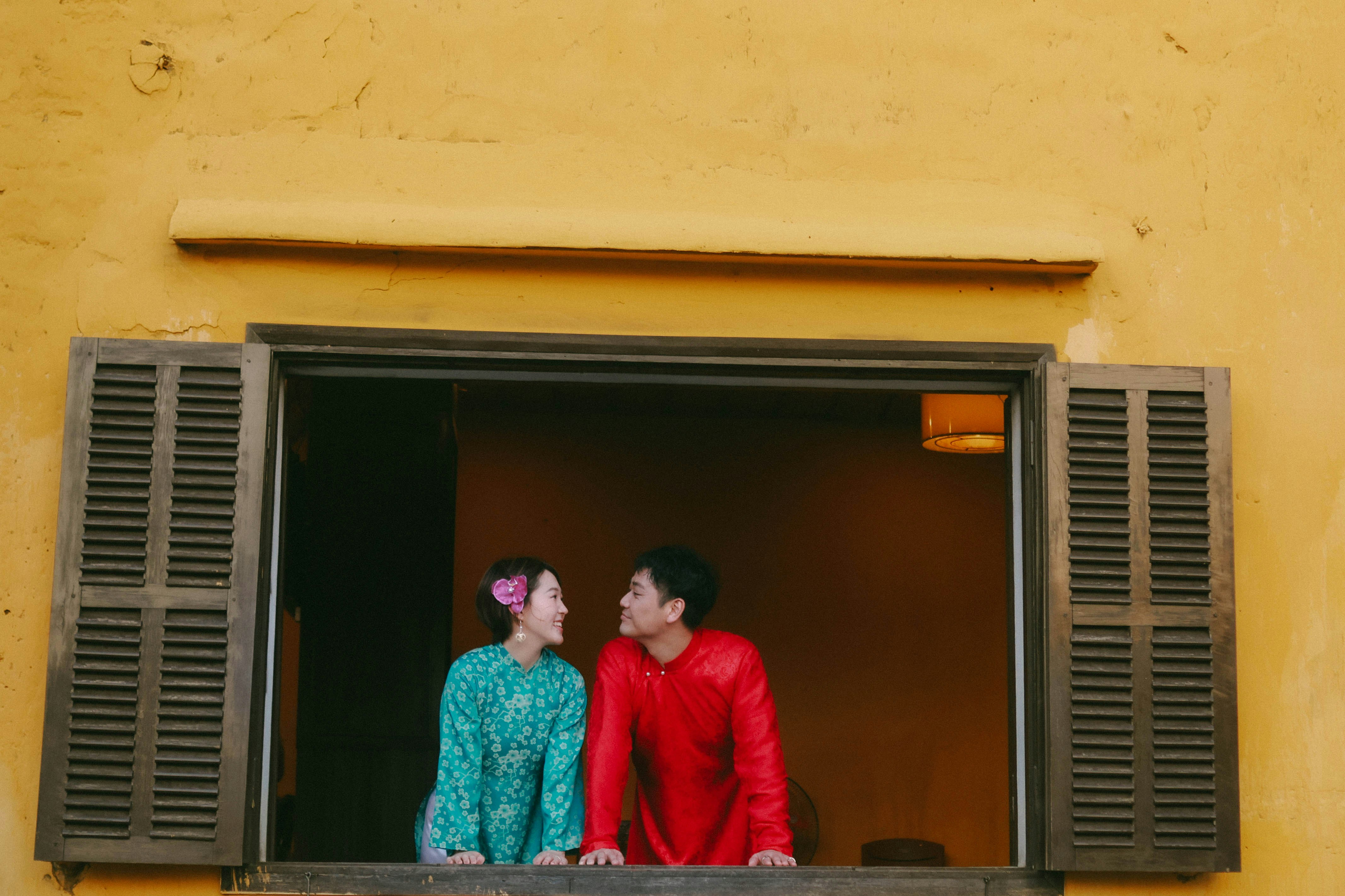 Window of Color: Two in Traditional Attire Share a Moment on a Sunny Balcony