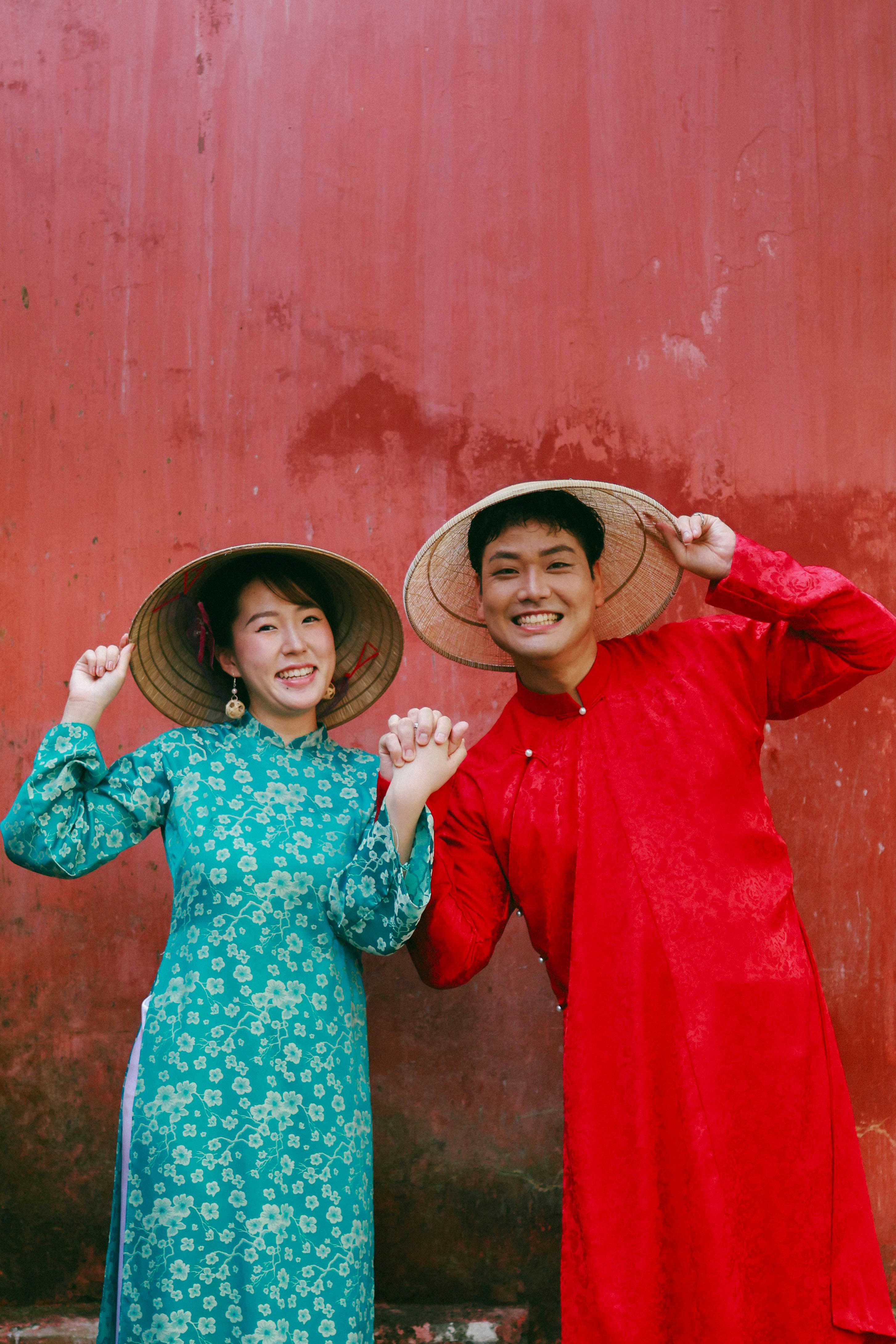 Joyful duet in traditional ao dai and conical hats against a red wall