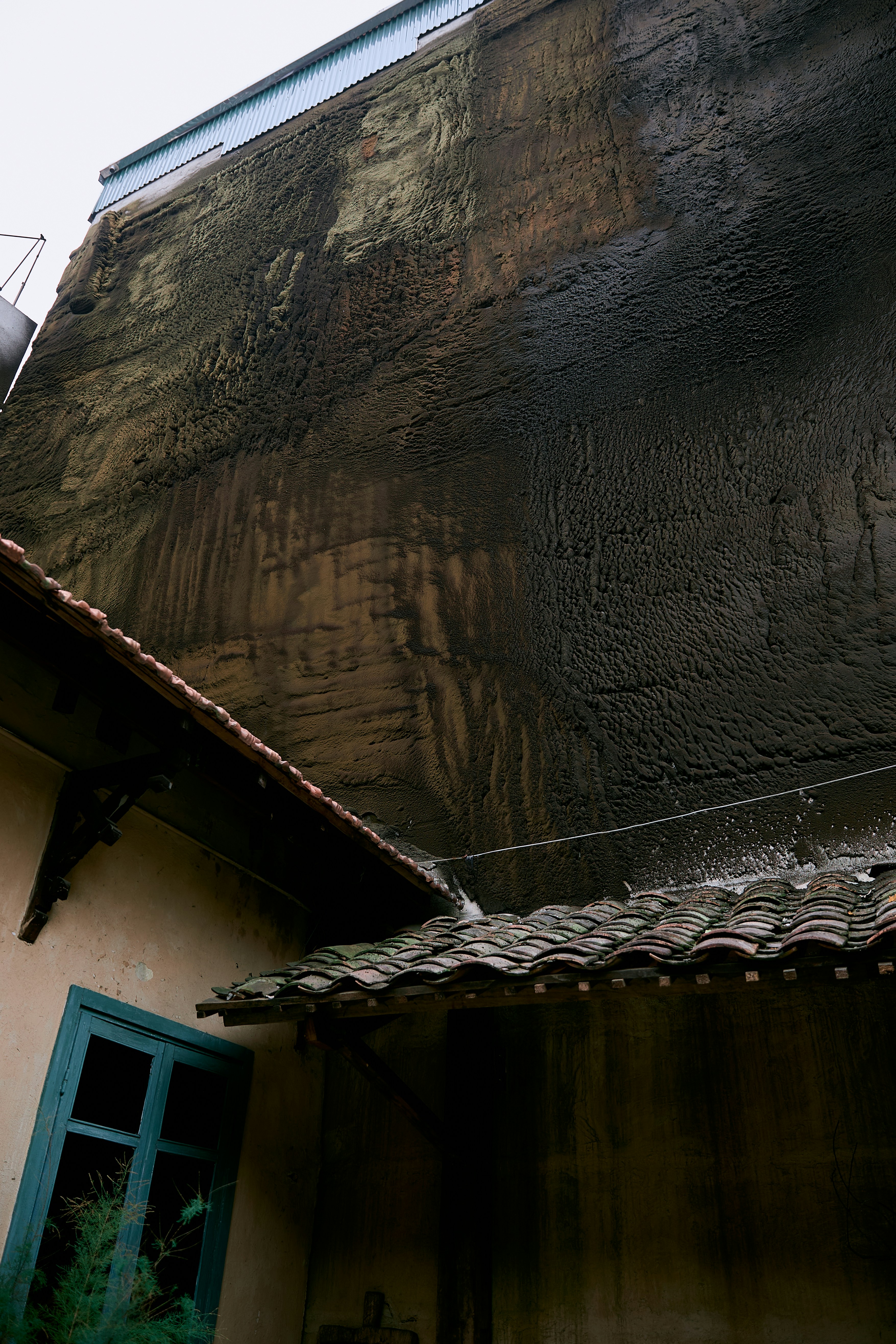 Urban Terrace Wall: Mossed Facade Reaching Over a Tile Roof