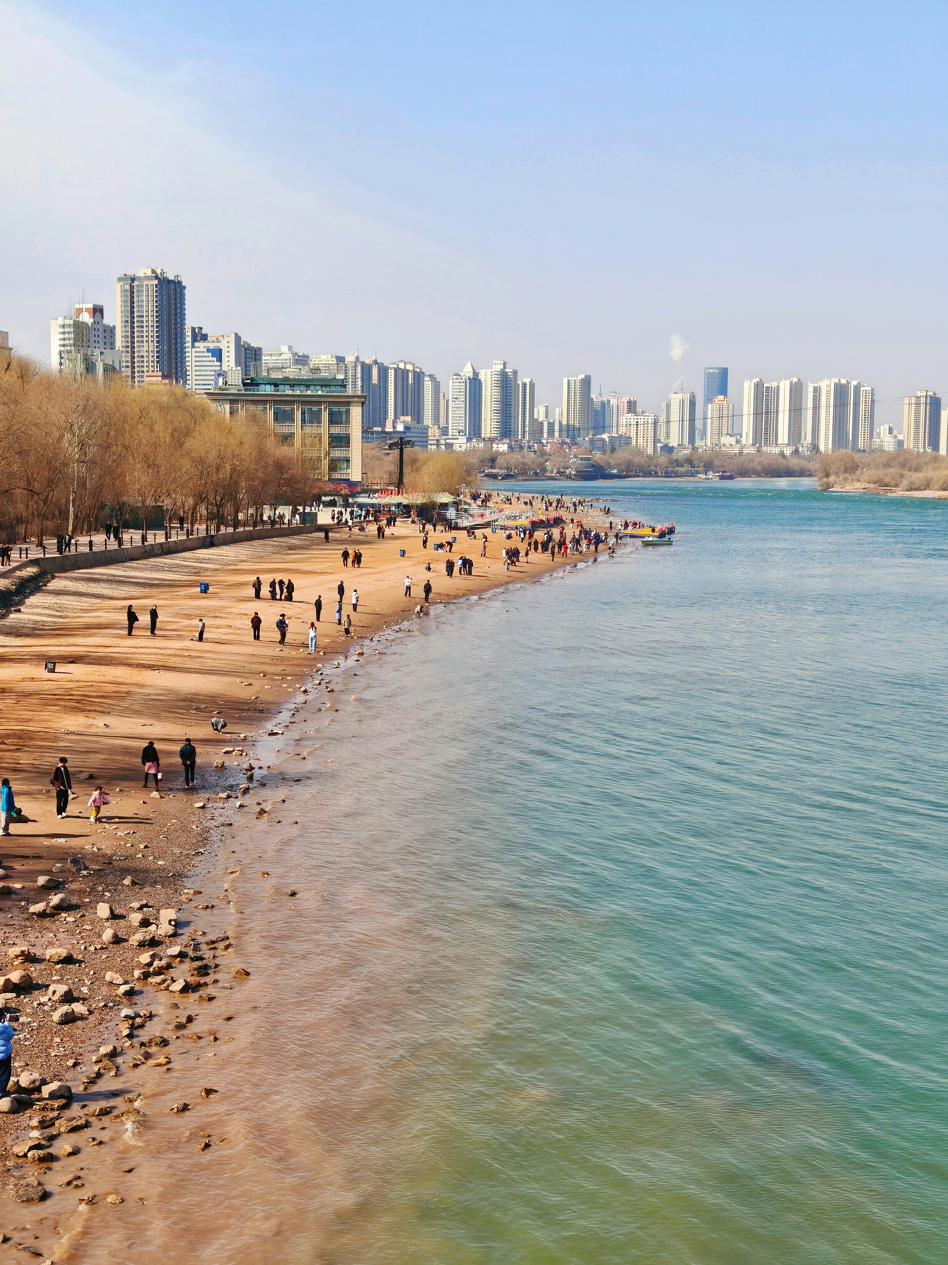 People strolling along a sandy beach with a city skyline.