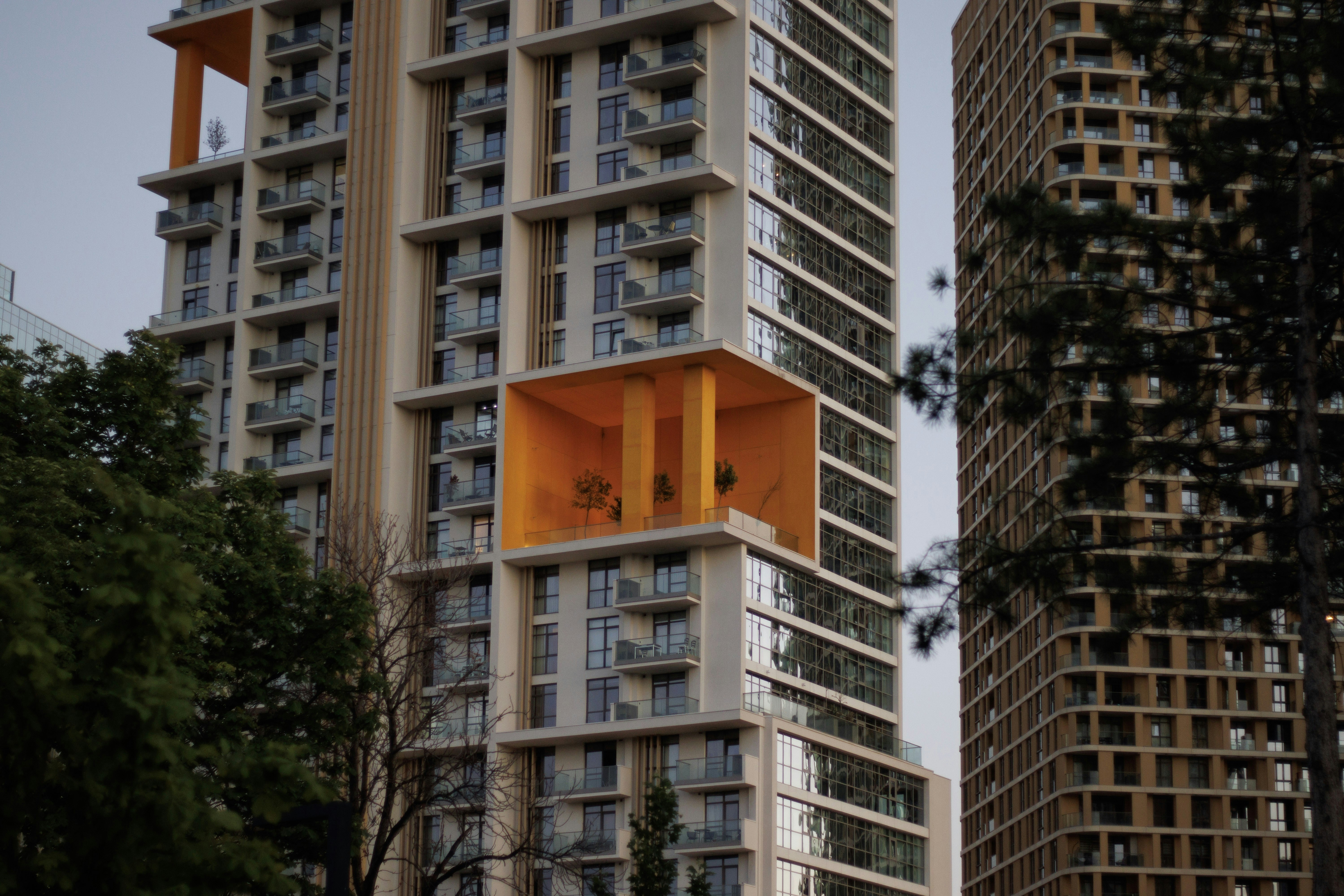 Urban Cubes: A Neon-Orange Balcony Cage Framed by Towers