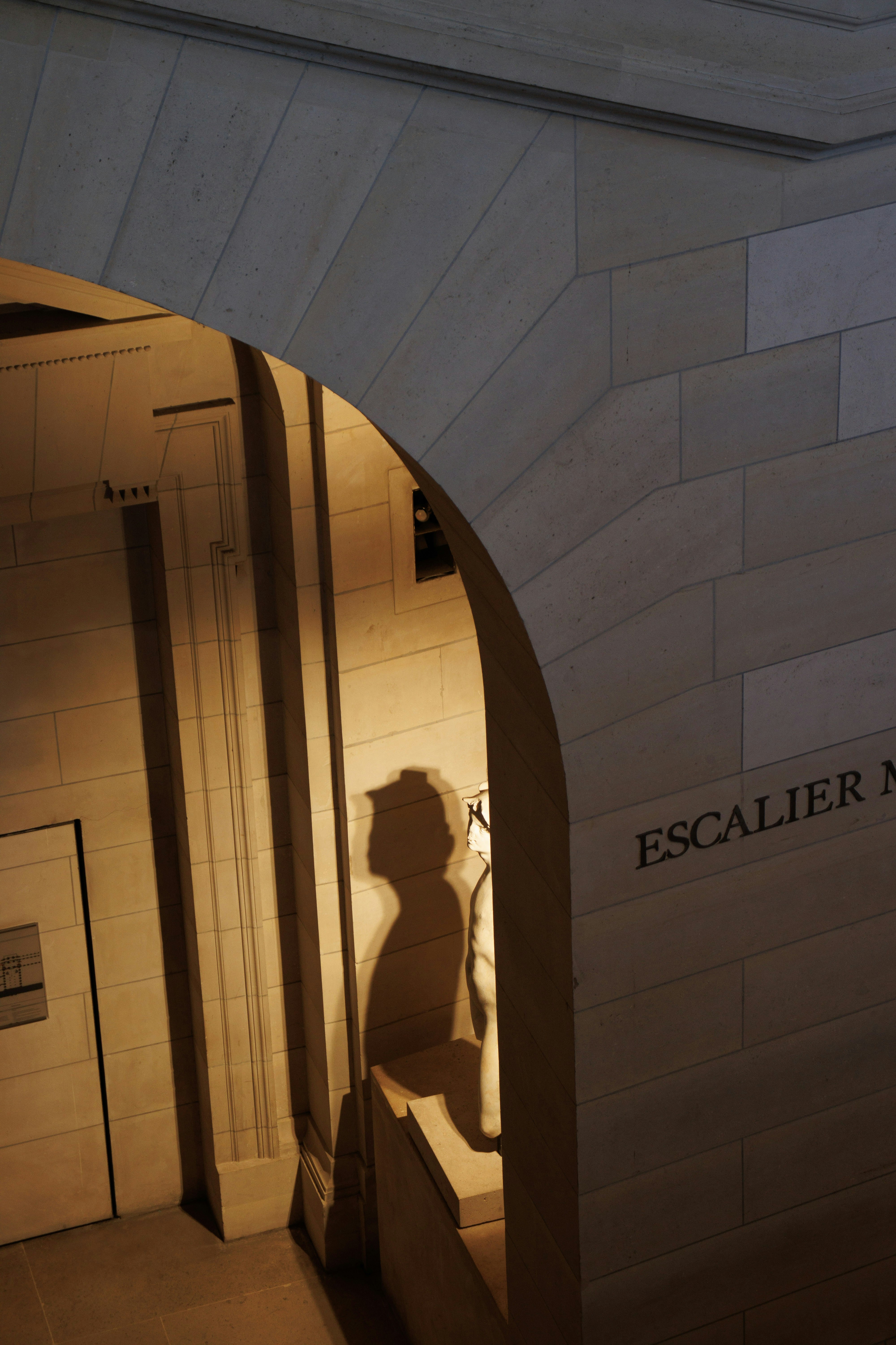 Shadowed entry: silhouetted figure within an arched museum façade