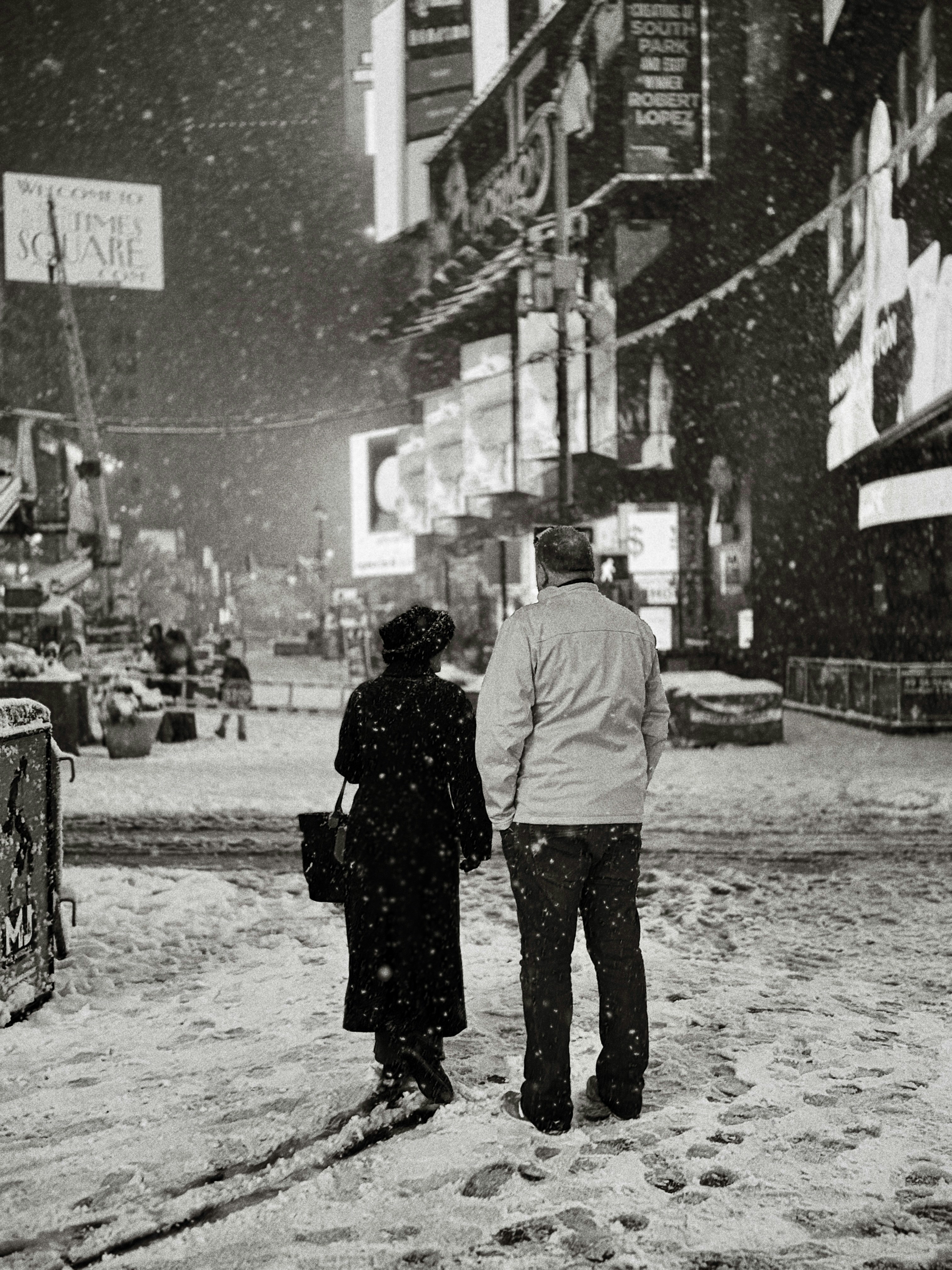 Snowy Evening in Times Square: A Couple Walking Beneath Falling Flakes