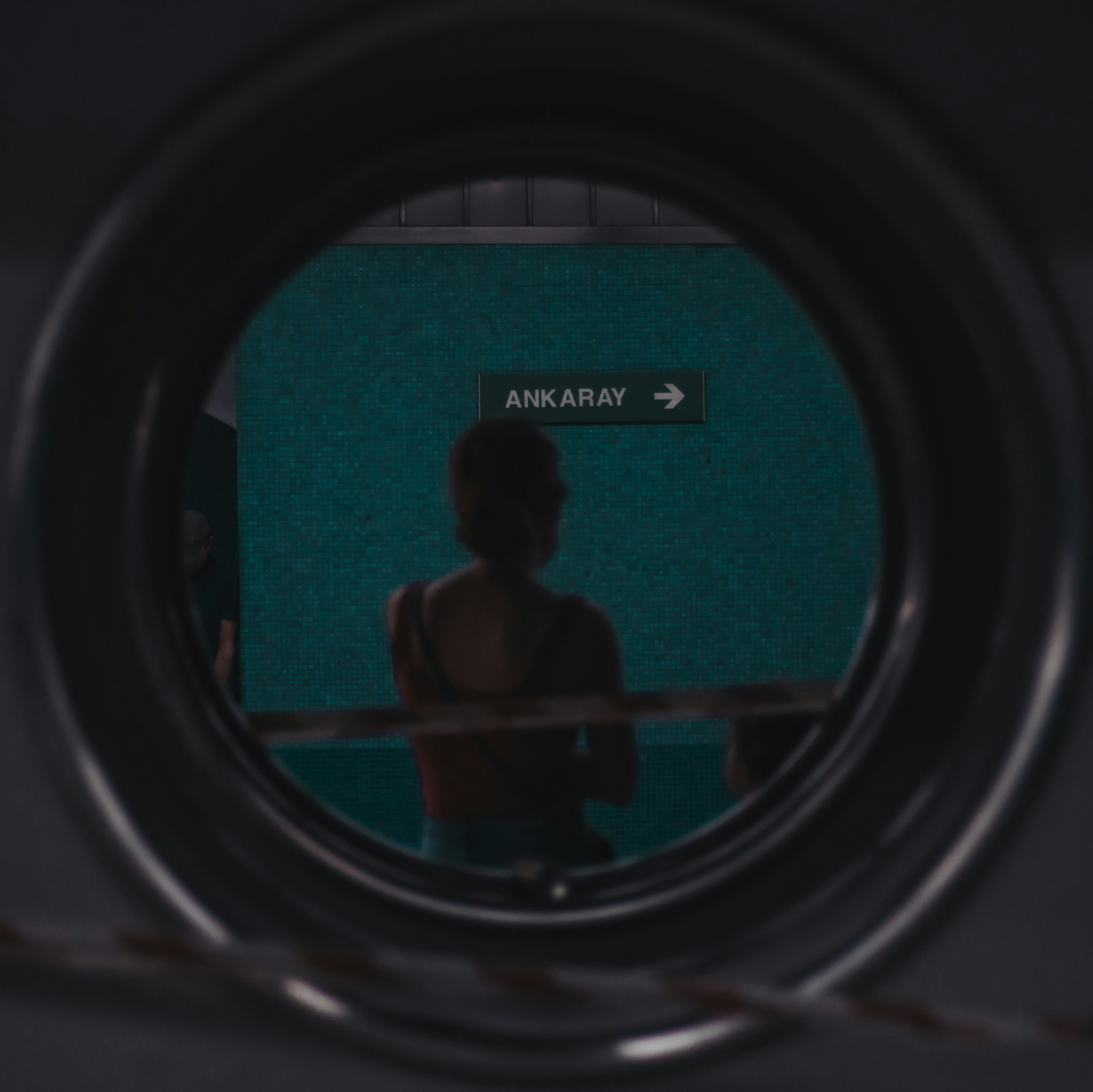 Through the Circular Frame: A Quiet Backlit Figure at the Exit Sign