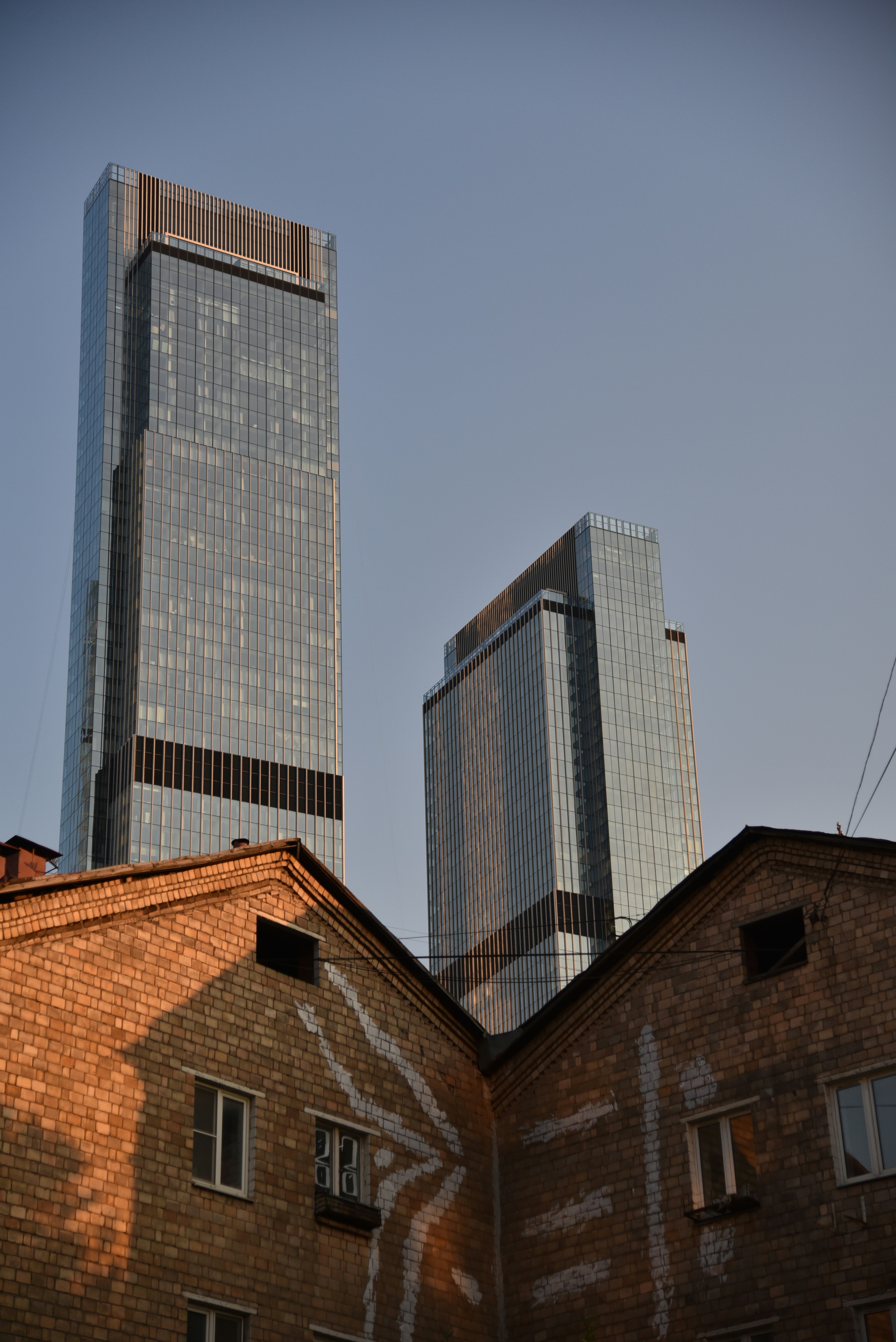 City Ghosts: Two Glass Towers Rise Over Brick Rooflines