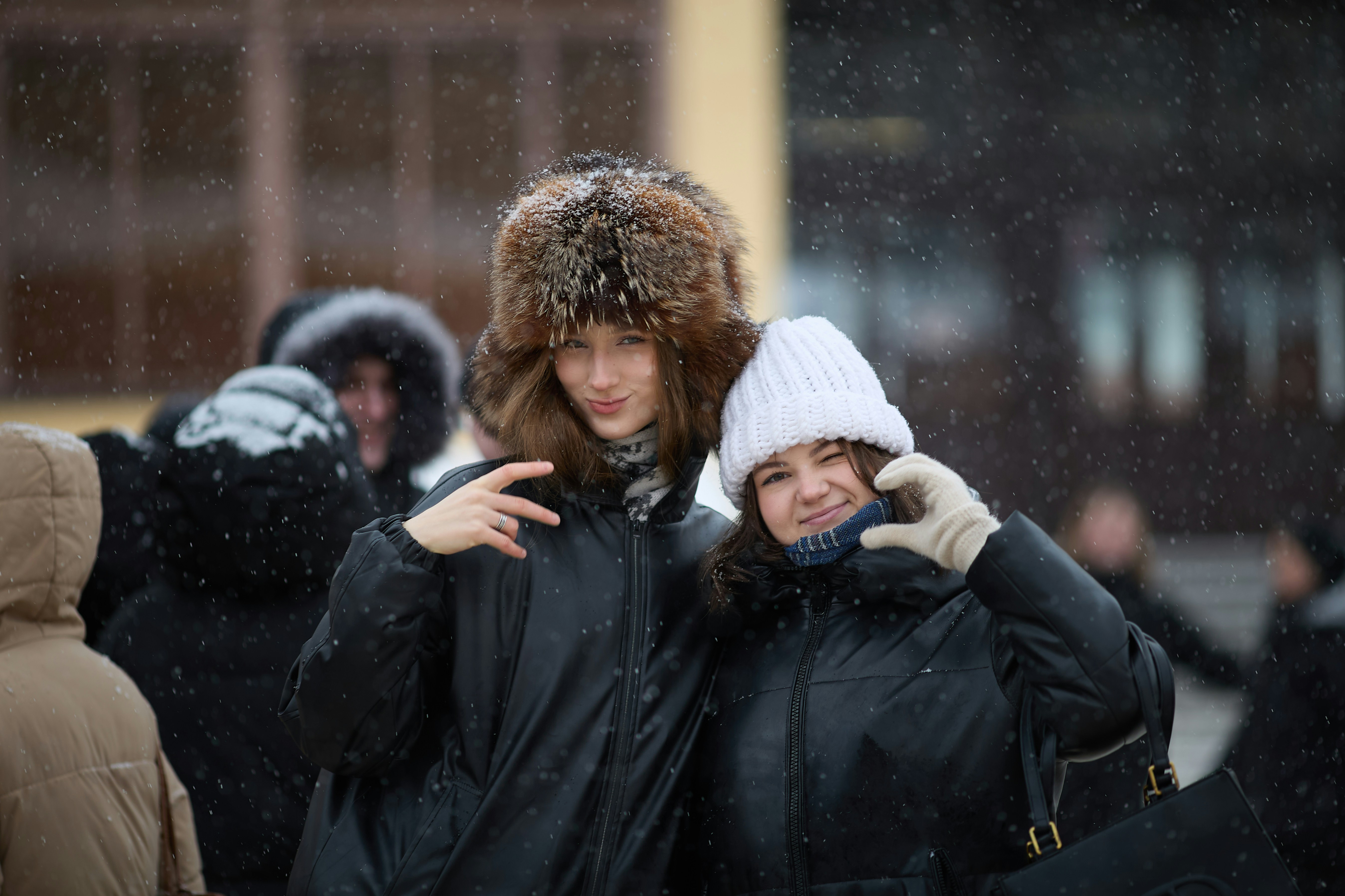 Snowy duo: playful smiles under warm hoods in a flurry
