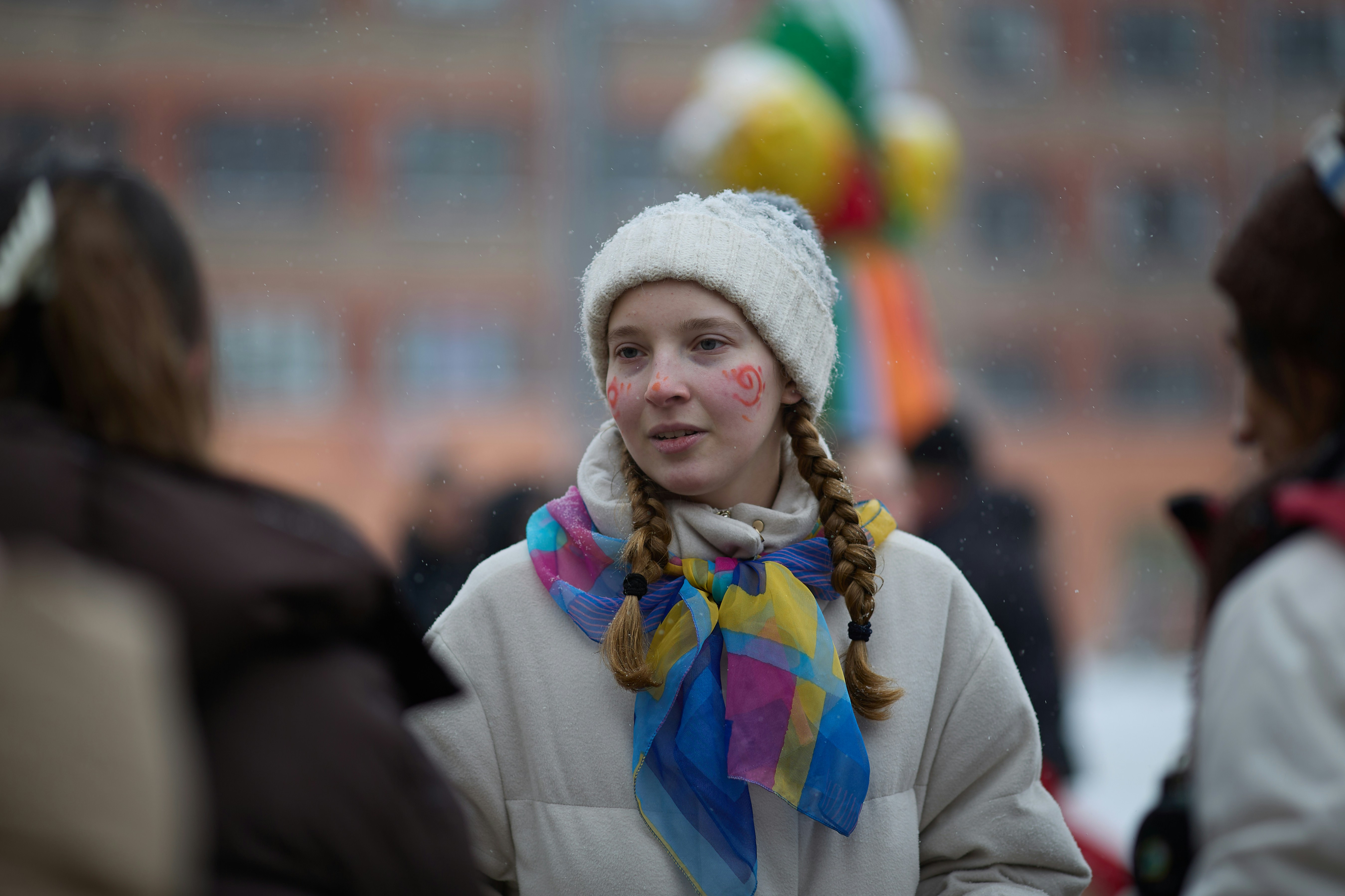 Winter festival portrait of a girl with braided hair and painted cheek in soft snowfall