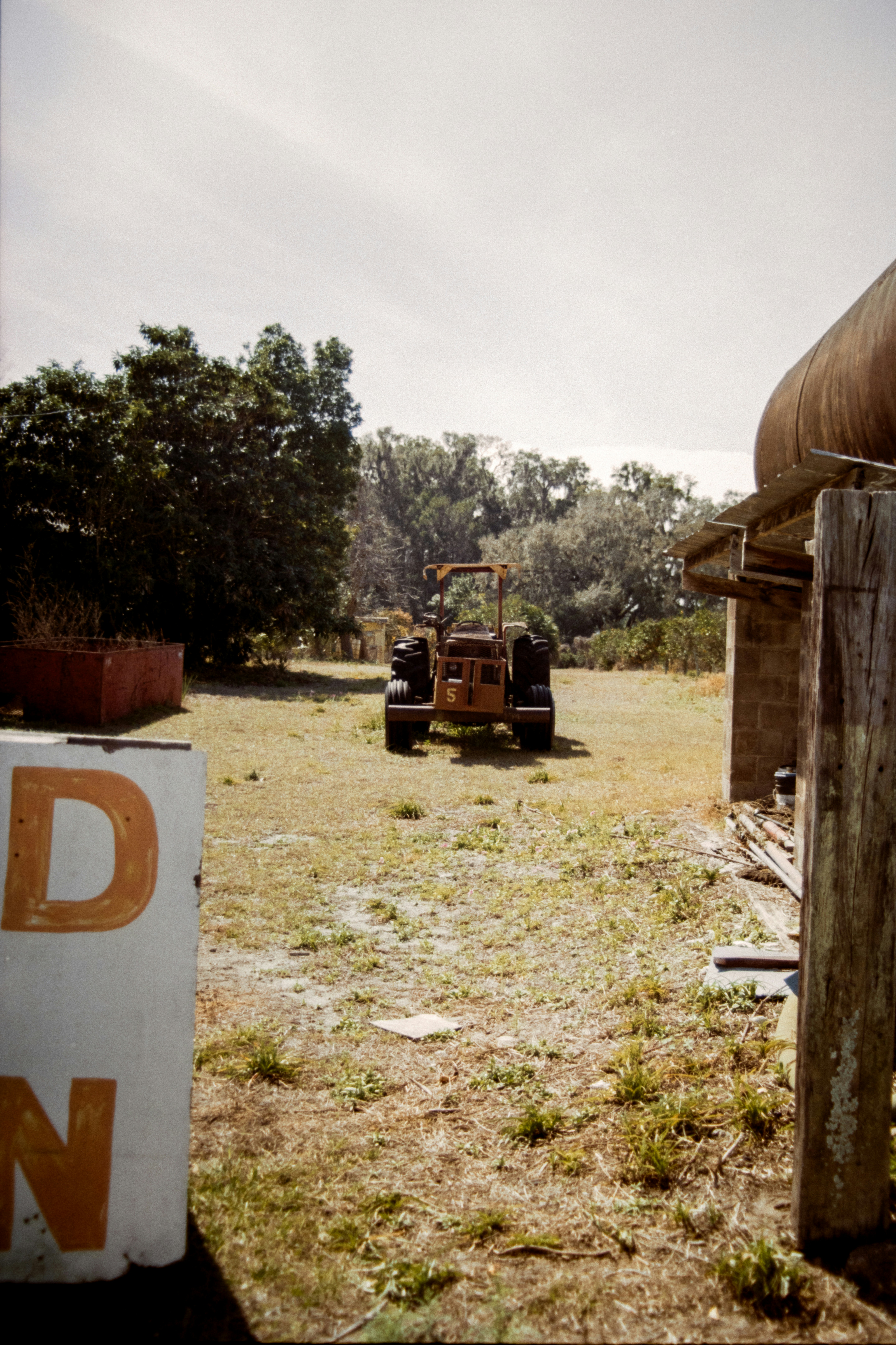 Old Tractor Resting Under a Shaded Shelter on a Sunlit Farmyard