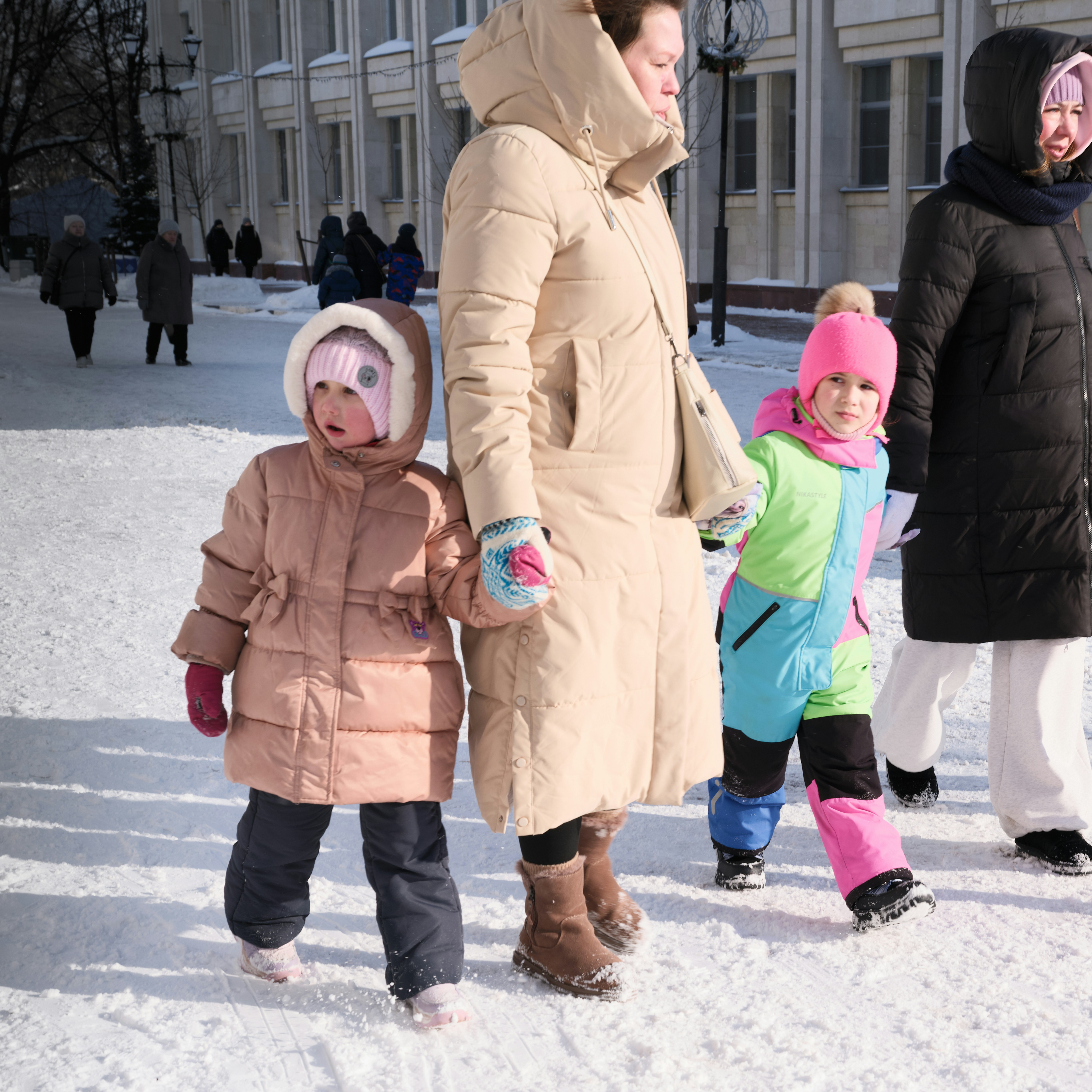 Winter parade: a mother guides two children across a snowy plaza