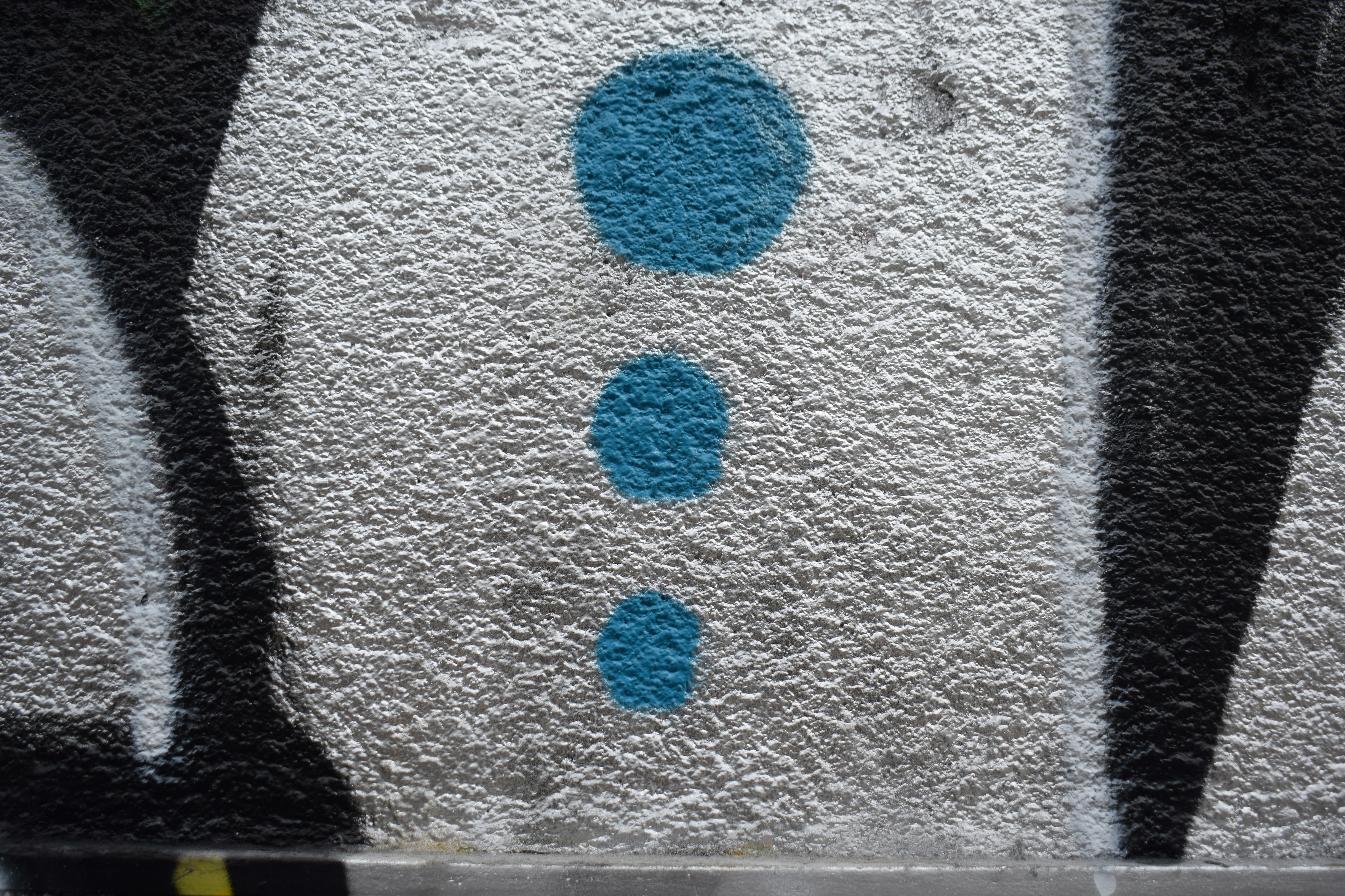 Blue Glyphs on Textured Concrete: A Vertical Stack of Dots Within Monochrome Graffiti