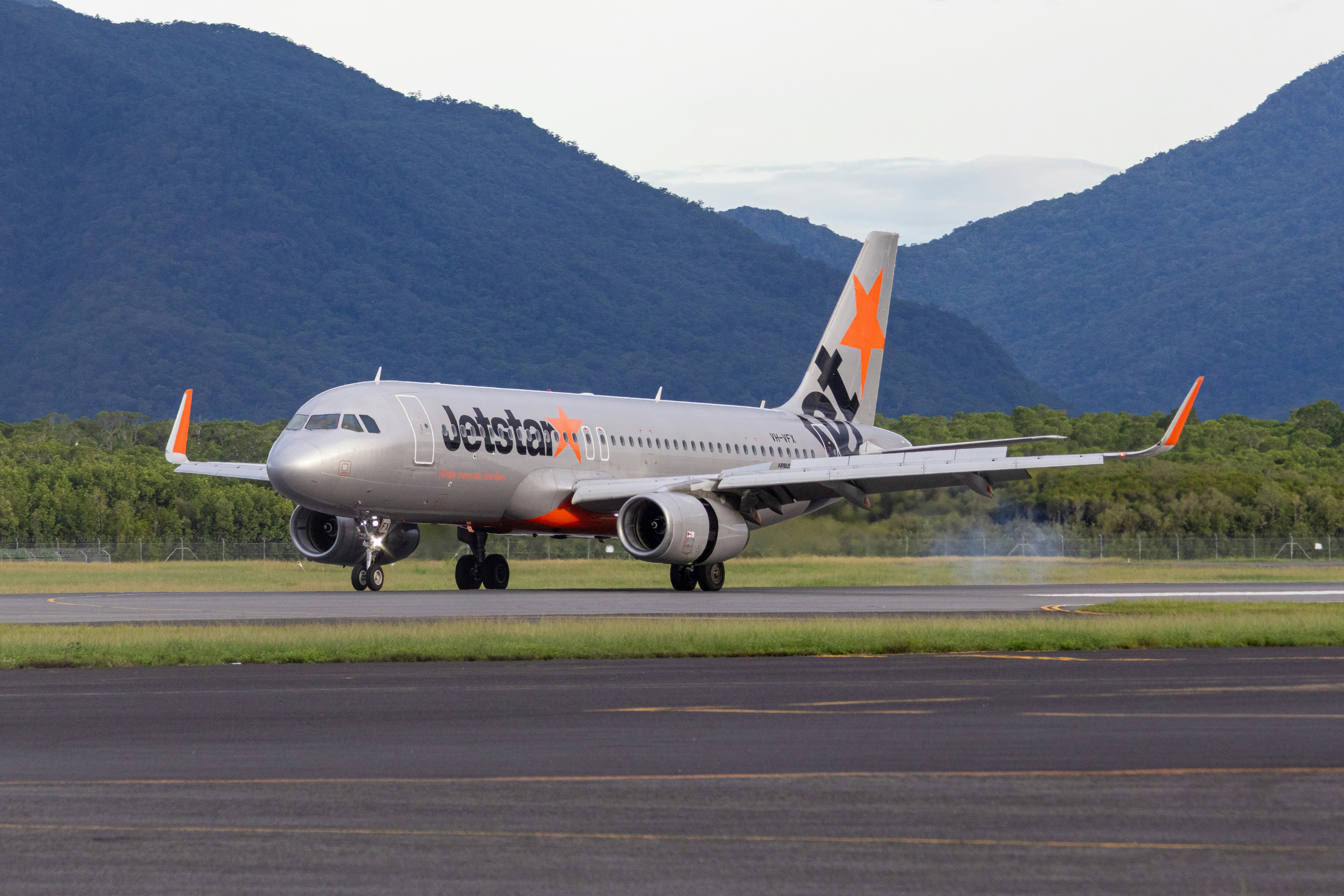 Jetstar at speed: a taxiing Airbus on a sunlit runway with volcanic backdrop