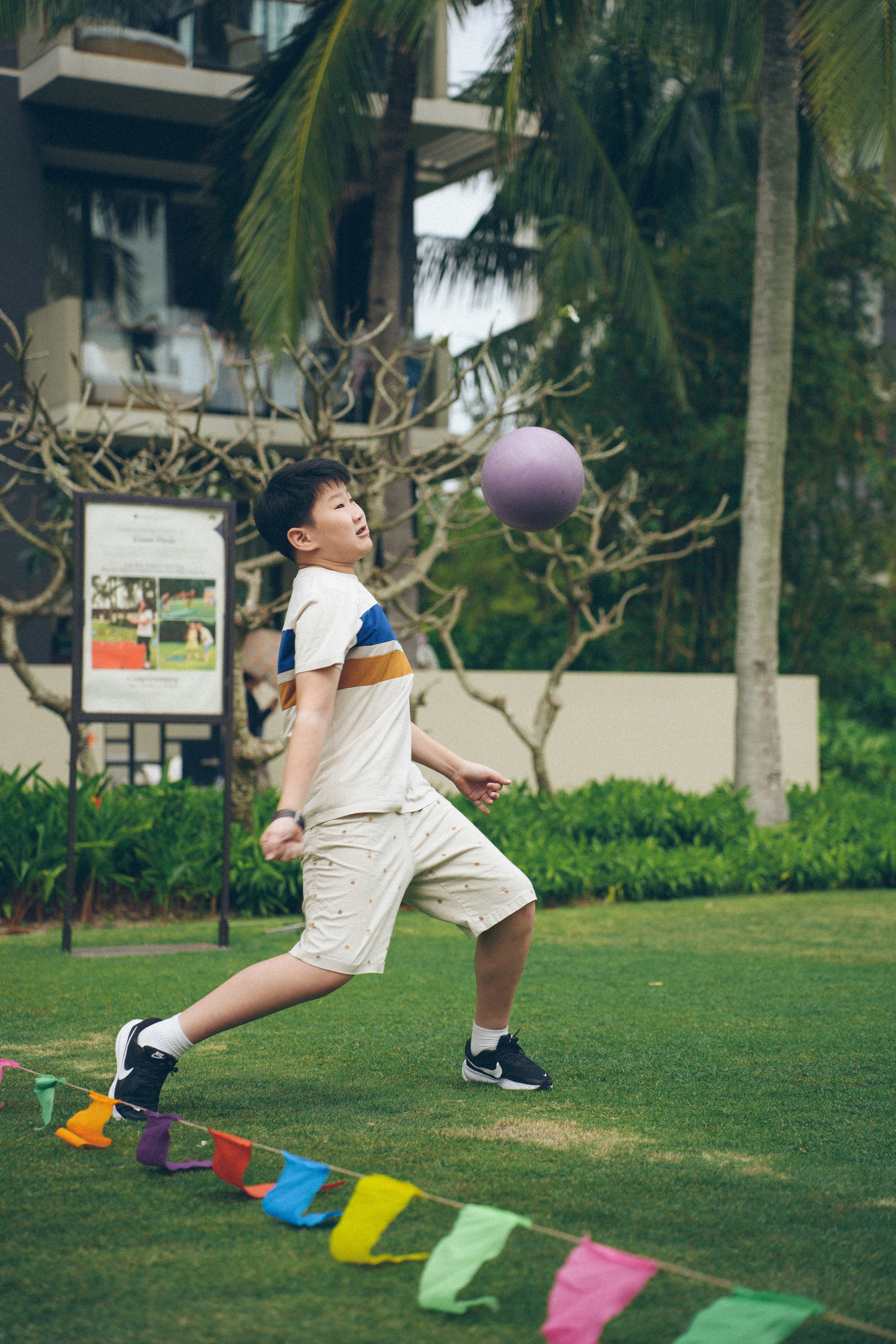 Green lawn, purple ball: a boy’s midair volley under tropical shade