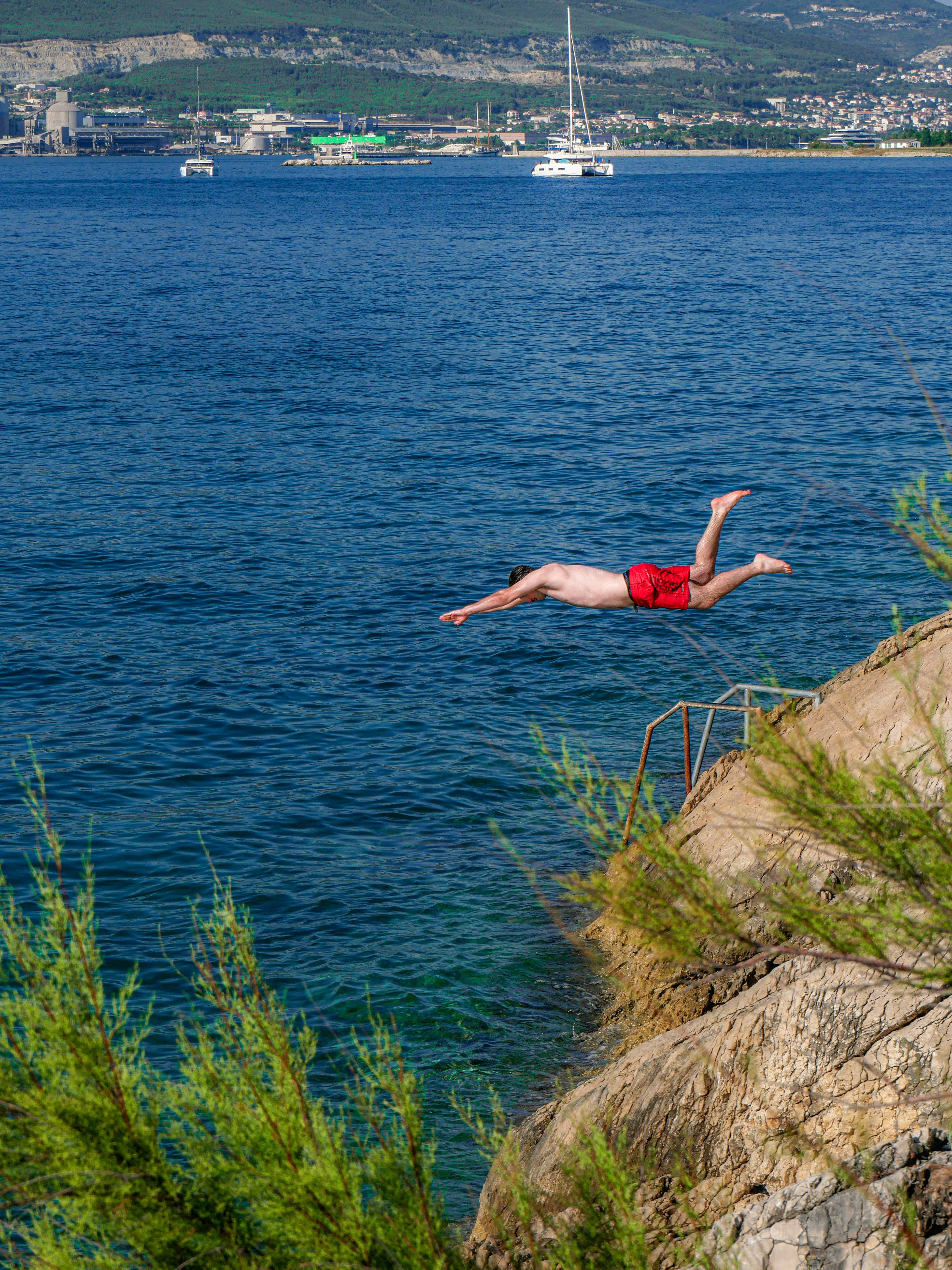 Diving man in red shorts sails above the turquoise sea