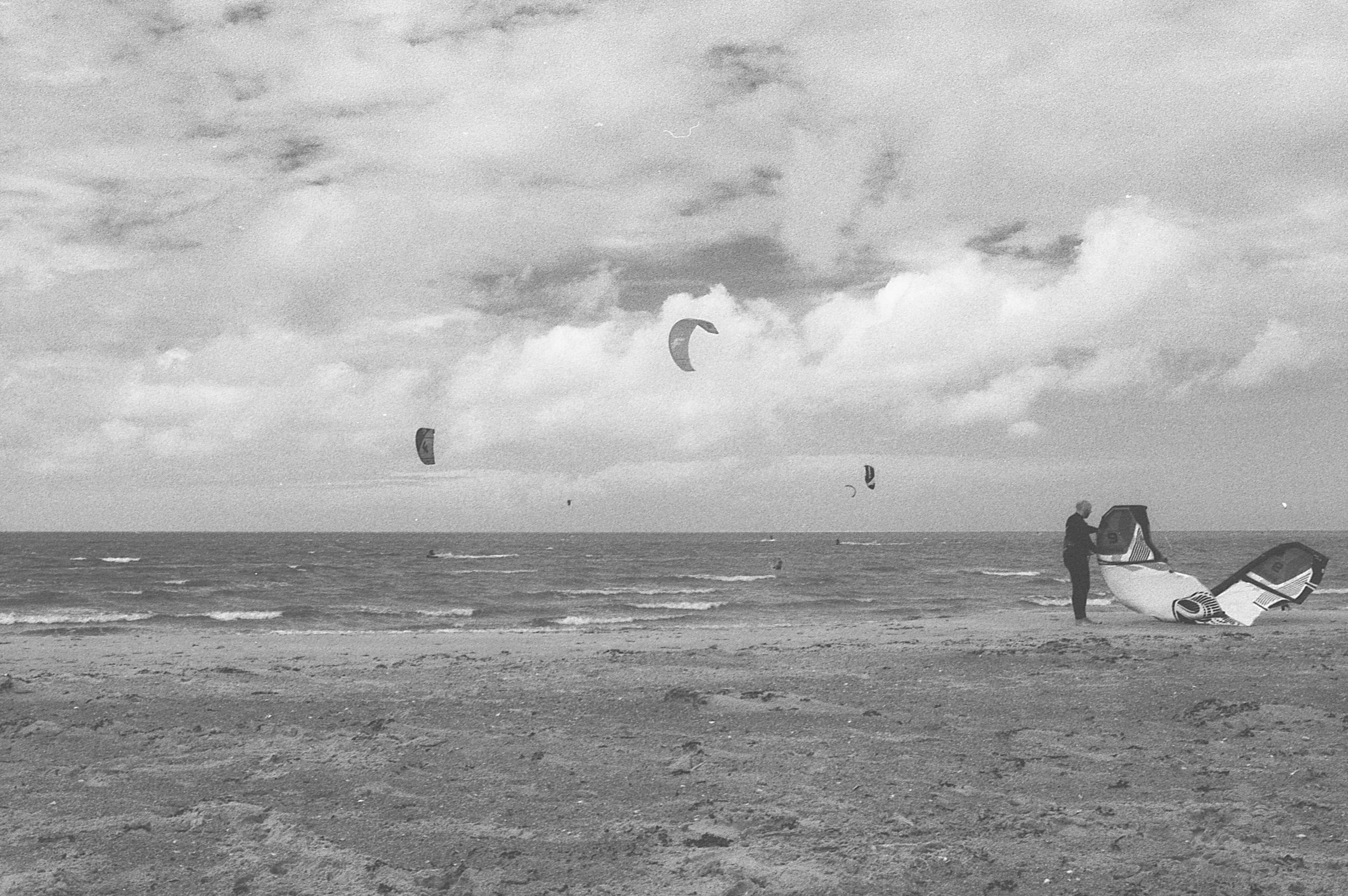 People kiteboarding on a cloudy day at the beach.