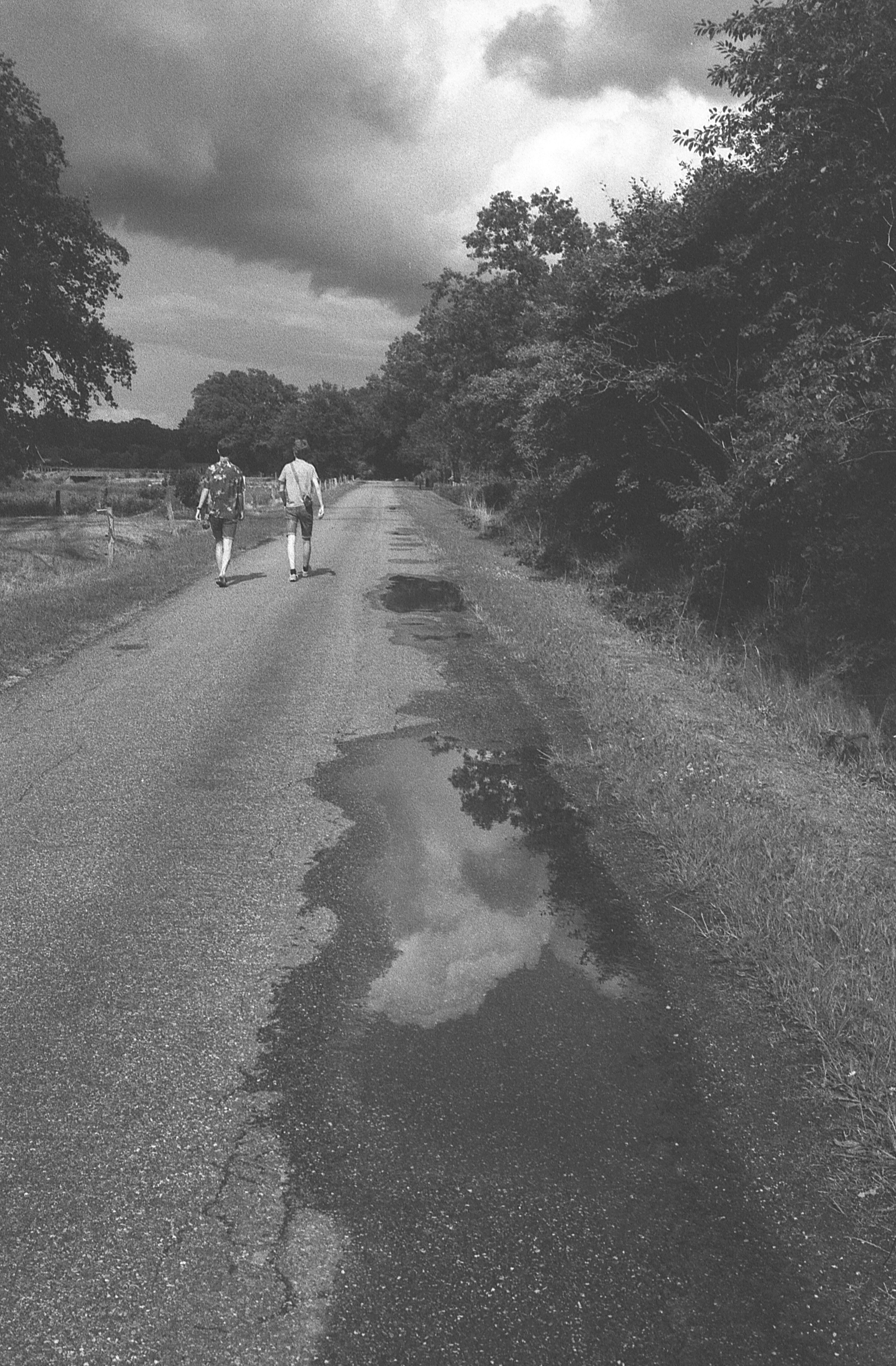 Two people walk down a wet road reflecting clouds