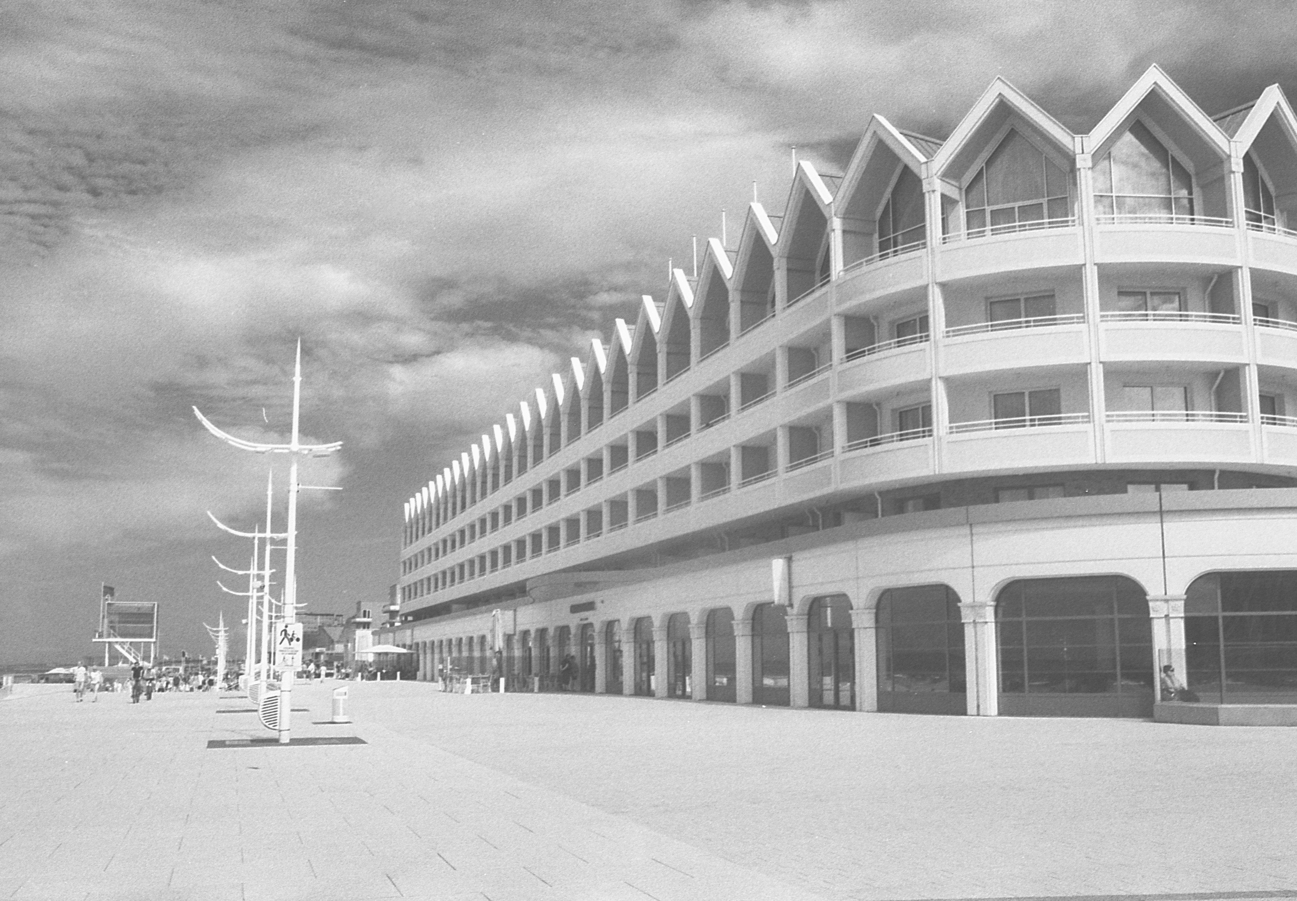 Modern hotel building on a sunny promenade with cloudy sky.