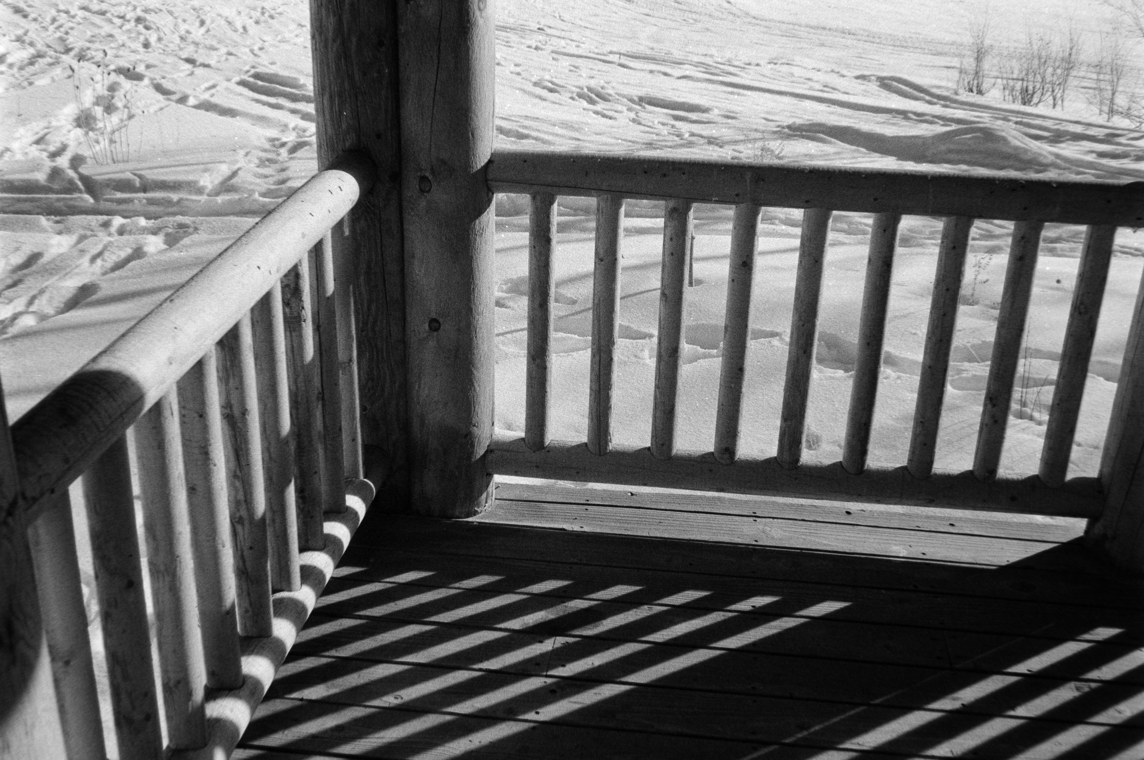 Shadowed Deck Railing Overlooking Snow: A Quiet Grayscale Scene