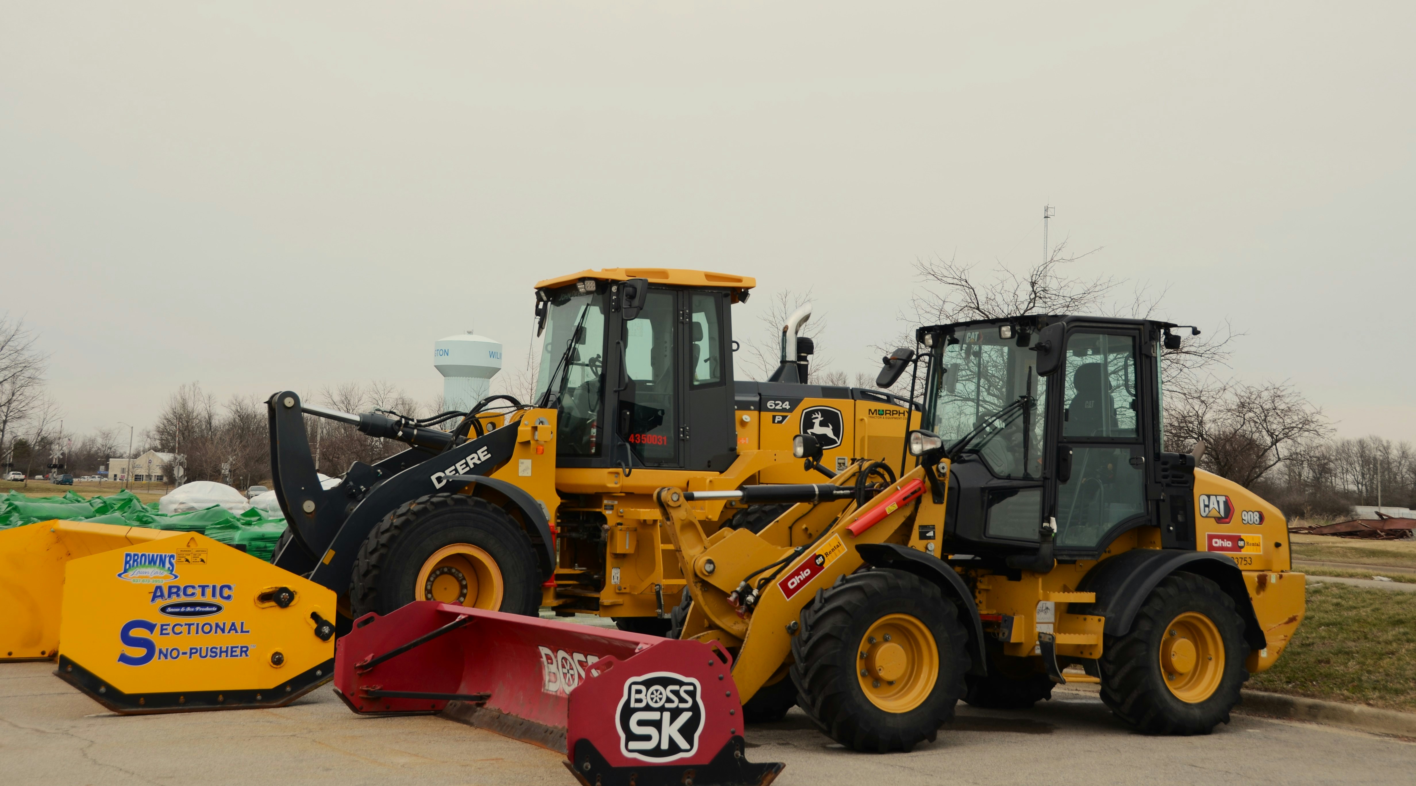 Industrial Pair: Two yellow loaders rest beside a red snow plow in a quiet yard