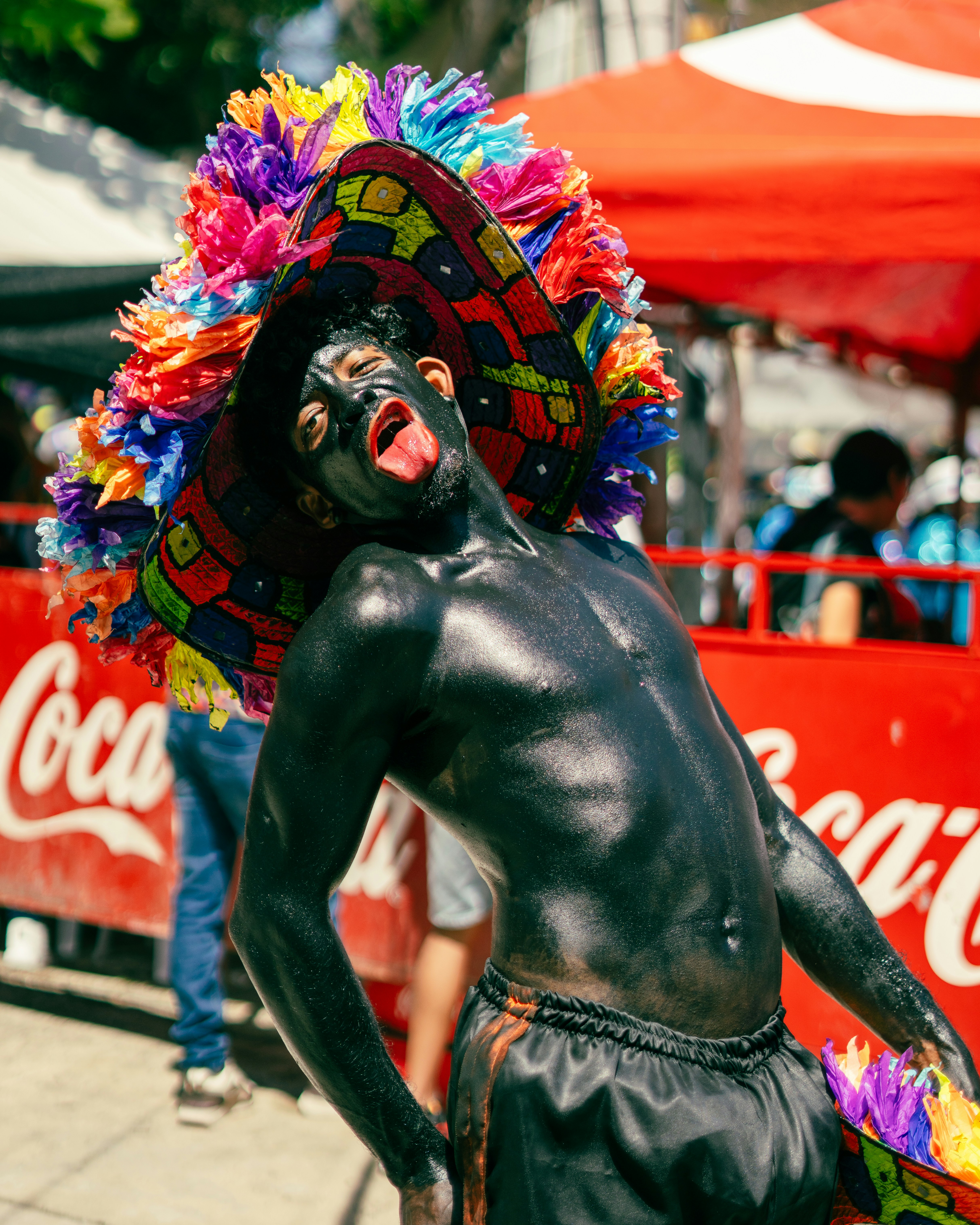 Color-Saturated Carnival: A Man in Charcoal Body Paint Under a Rainbow Headdress