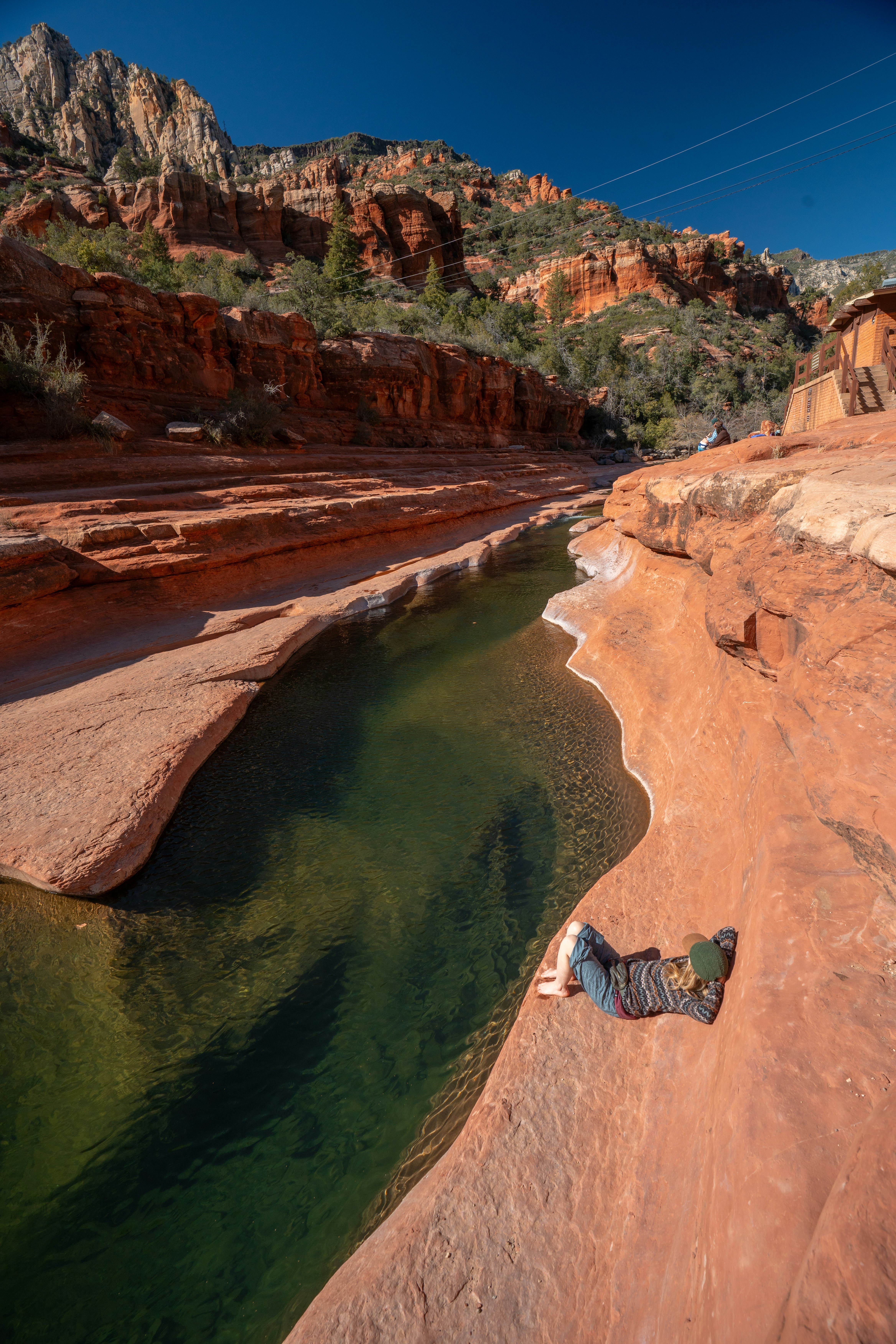 Person reclining on the red rock by the emerald river in a canyon
