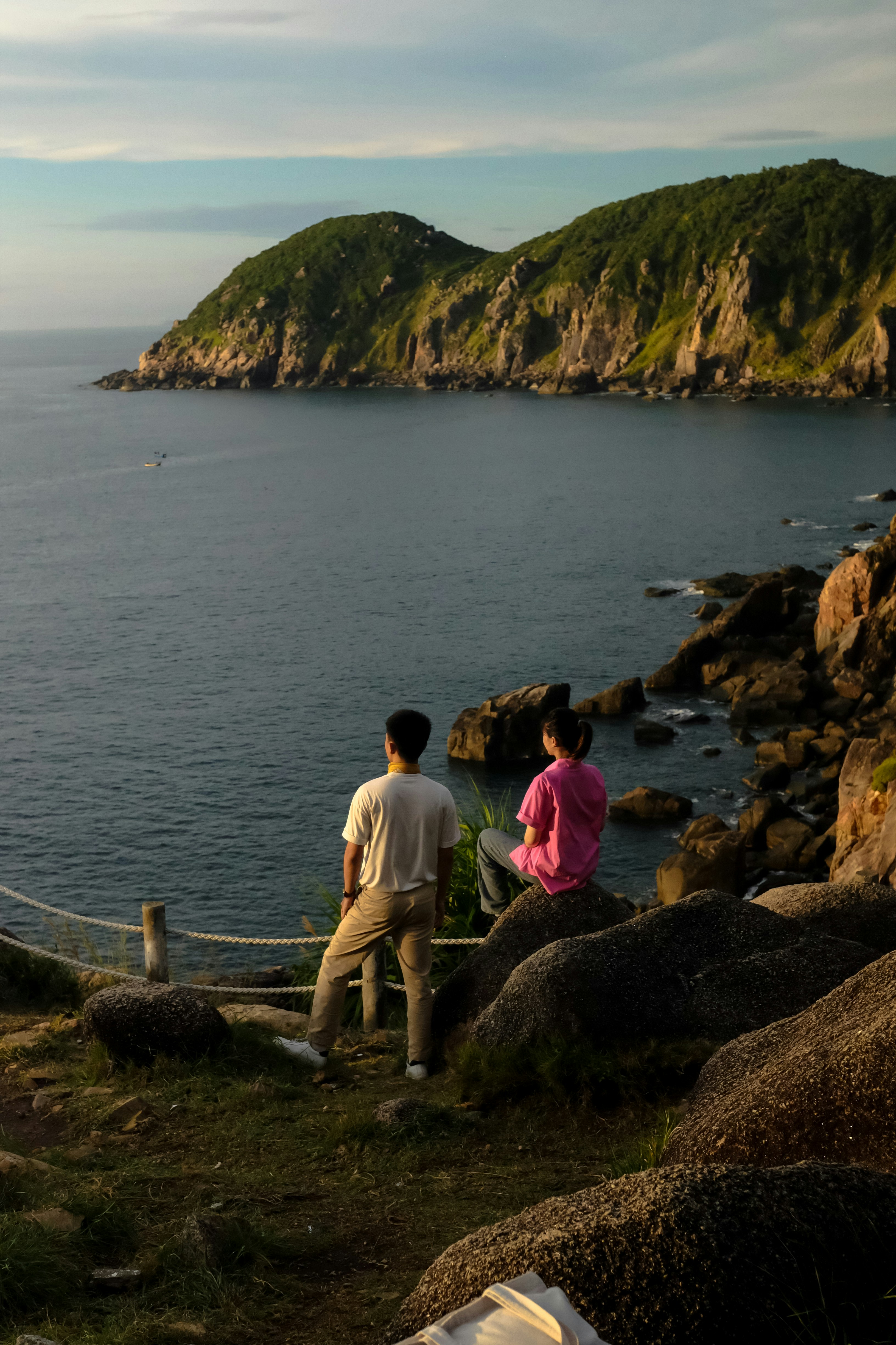 Two Visitors at a Cliffside Overlook as Evening Light Casts onto the Sea