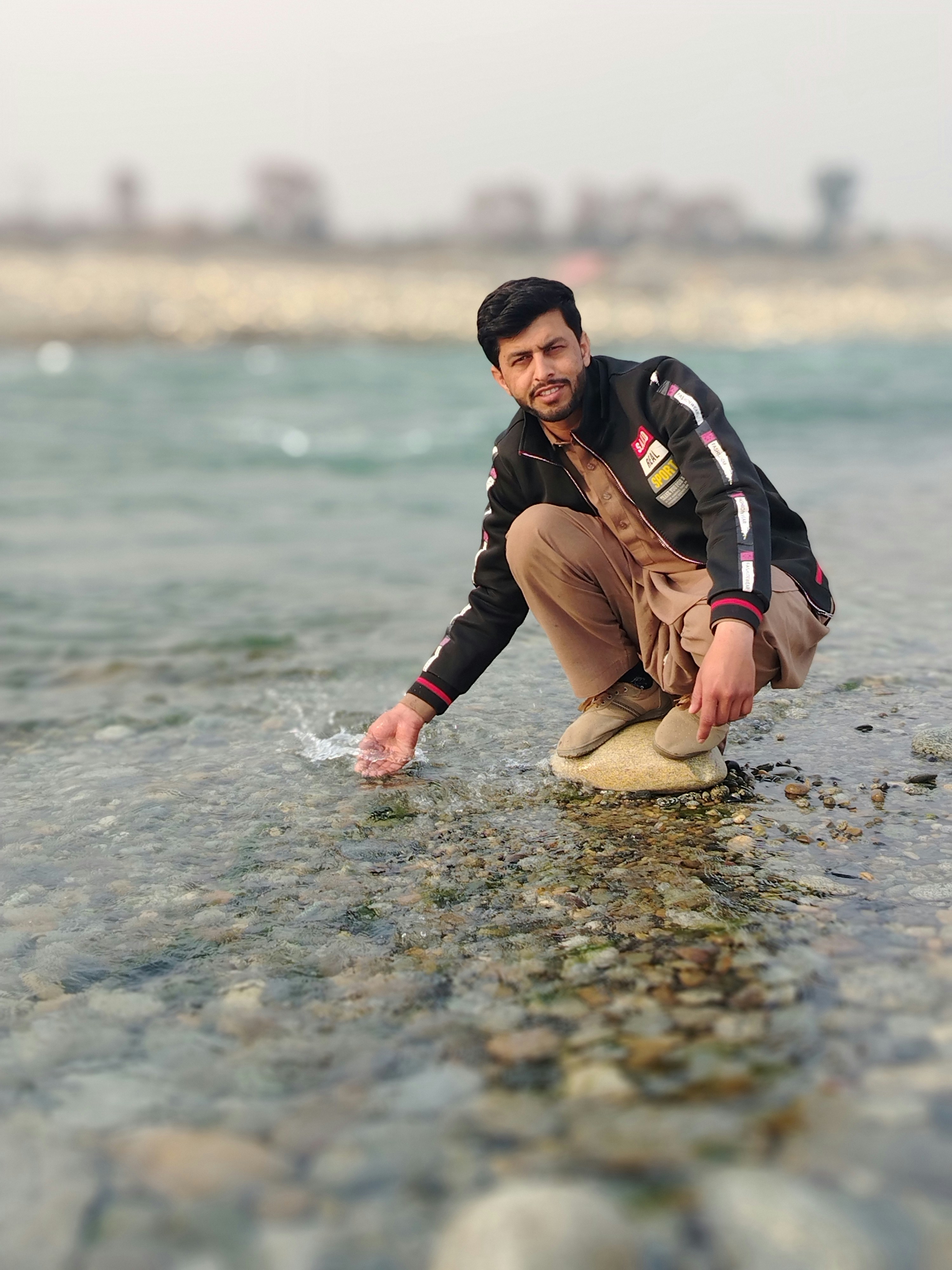 Man crouching by a clear river, touching water
