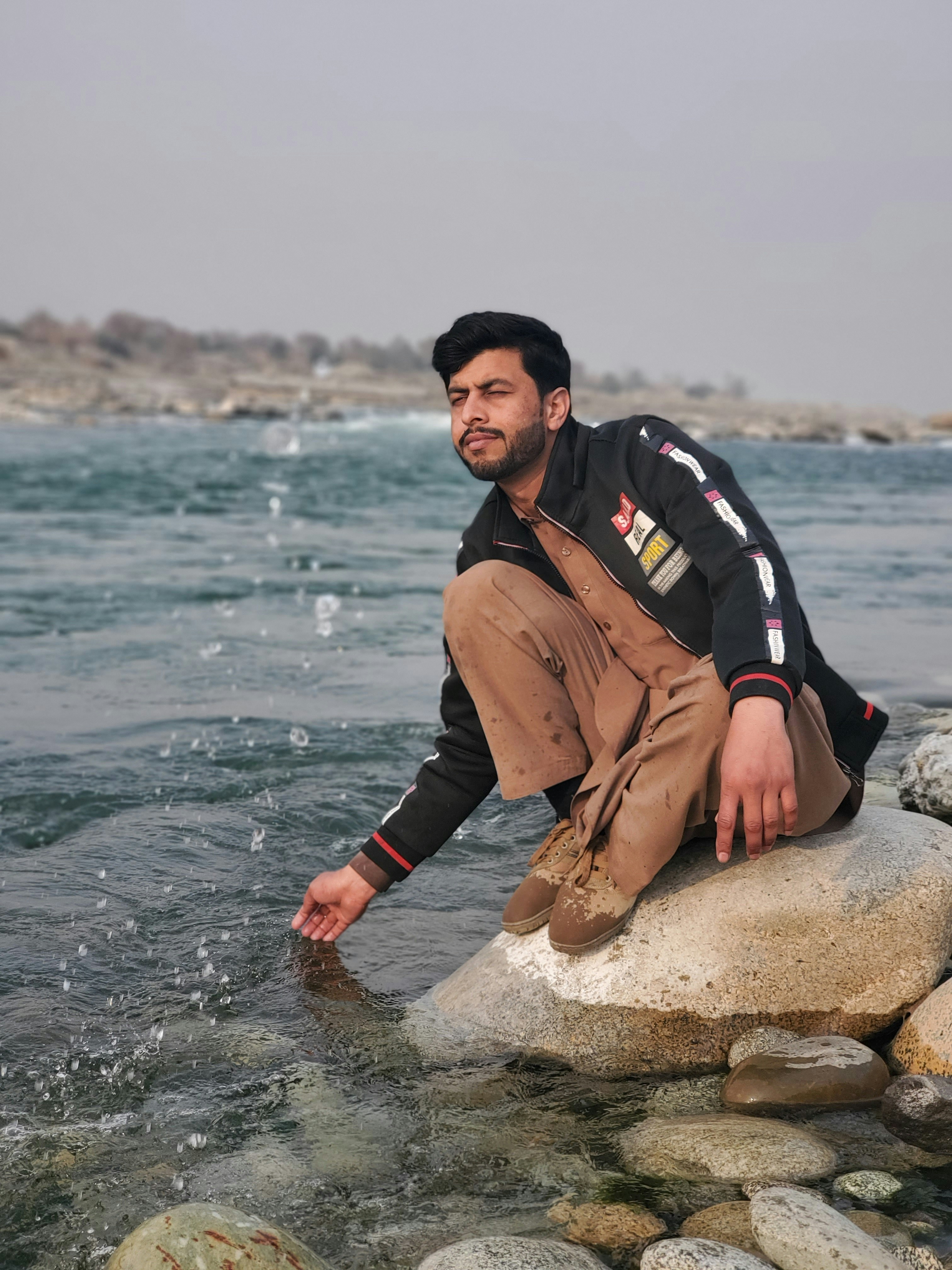 Man sitting on rocks by a river touching water
